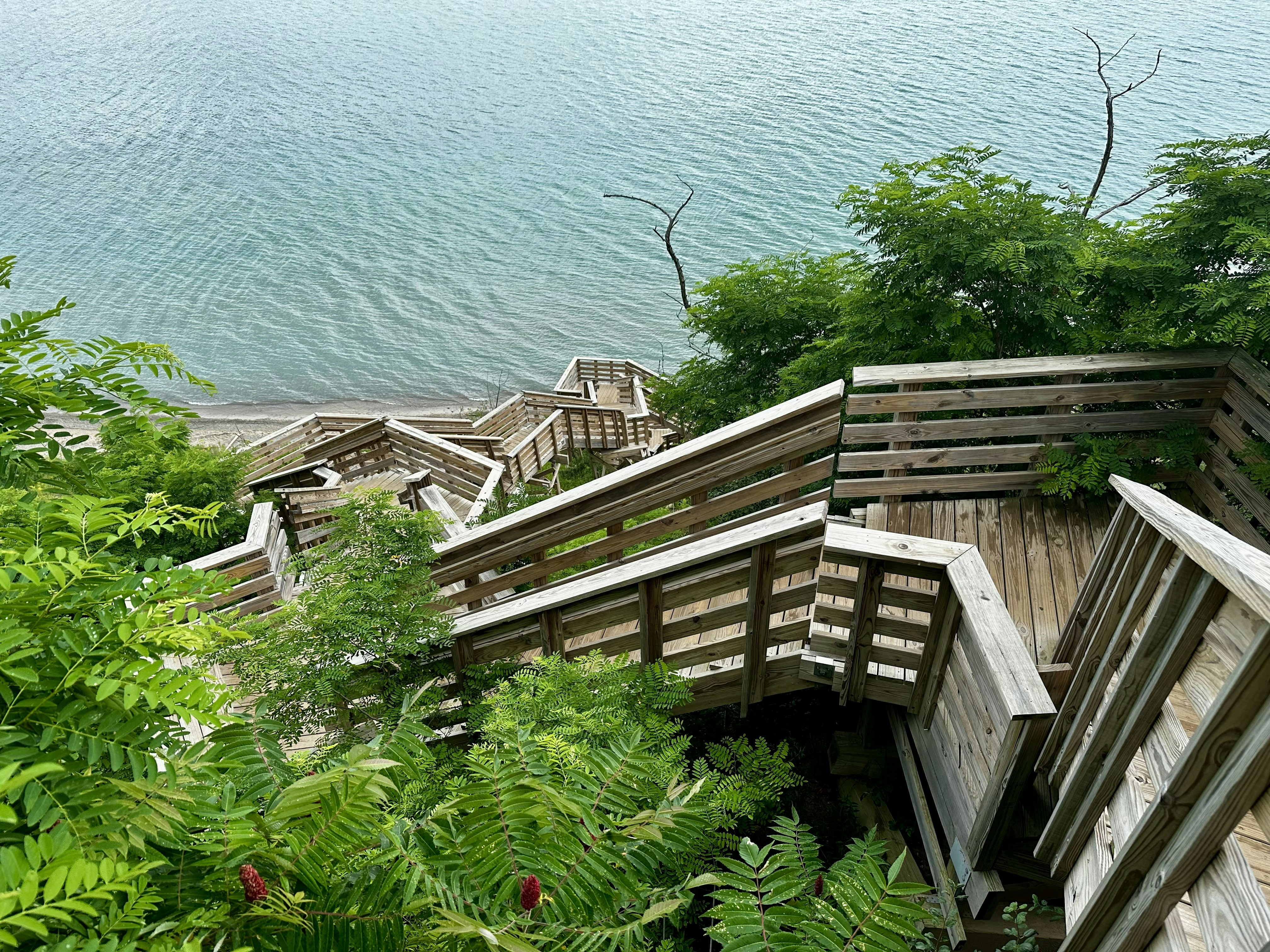 A wood staircase descending down the side of a bluff. | Wooden stairs lead down to a beautiful lake.