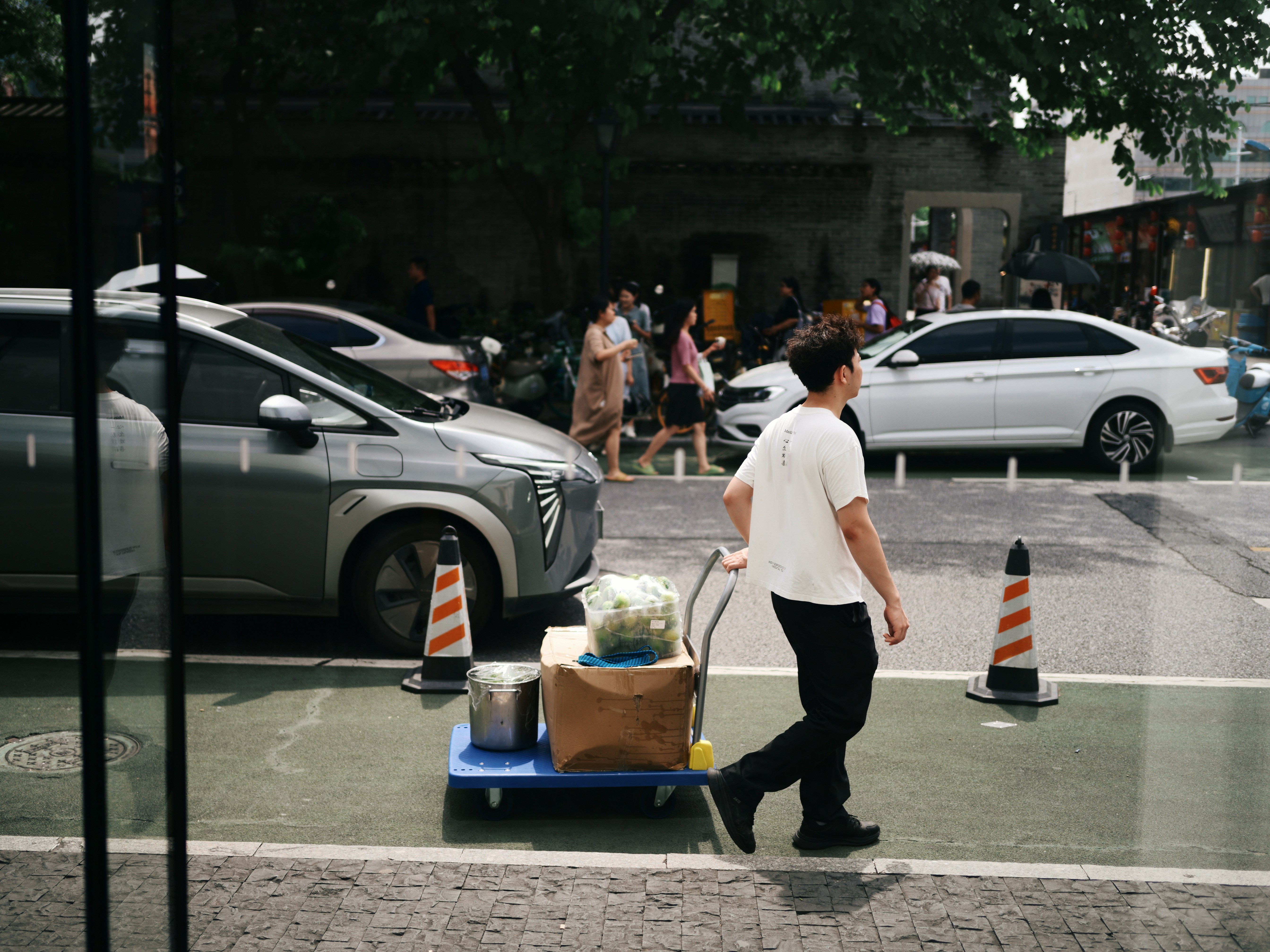 A man pushes a cart loaded with goods along a bustling street, surrounded by vehicles and pedestrians. The scene captures the vibrant energy of daily city life.