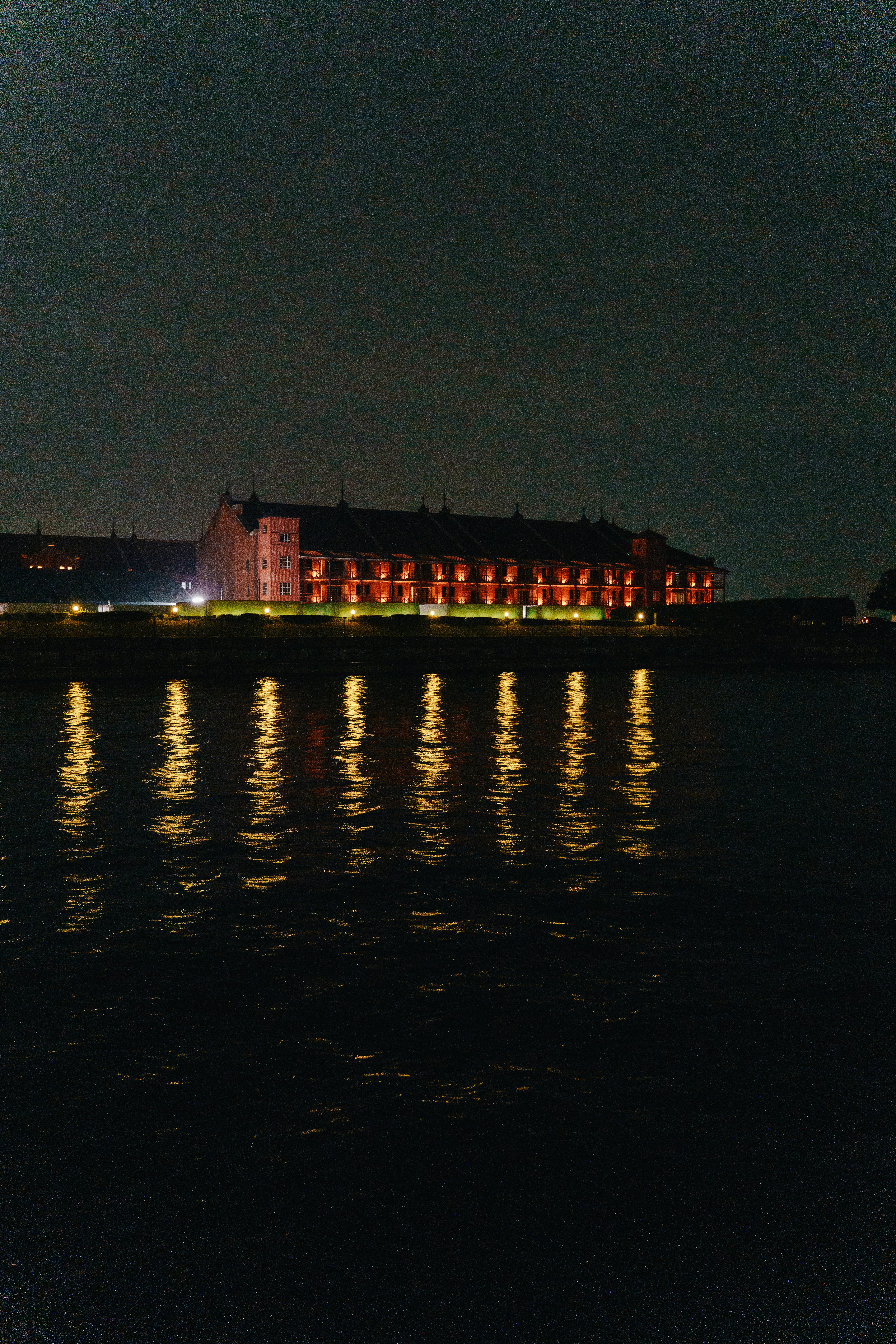 Golden Riverside Facade: Night-lit Warehouse by Reflected Water