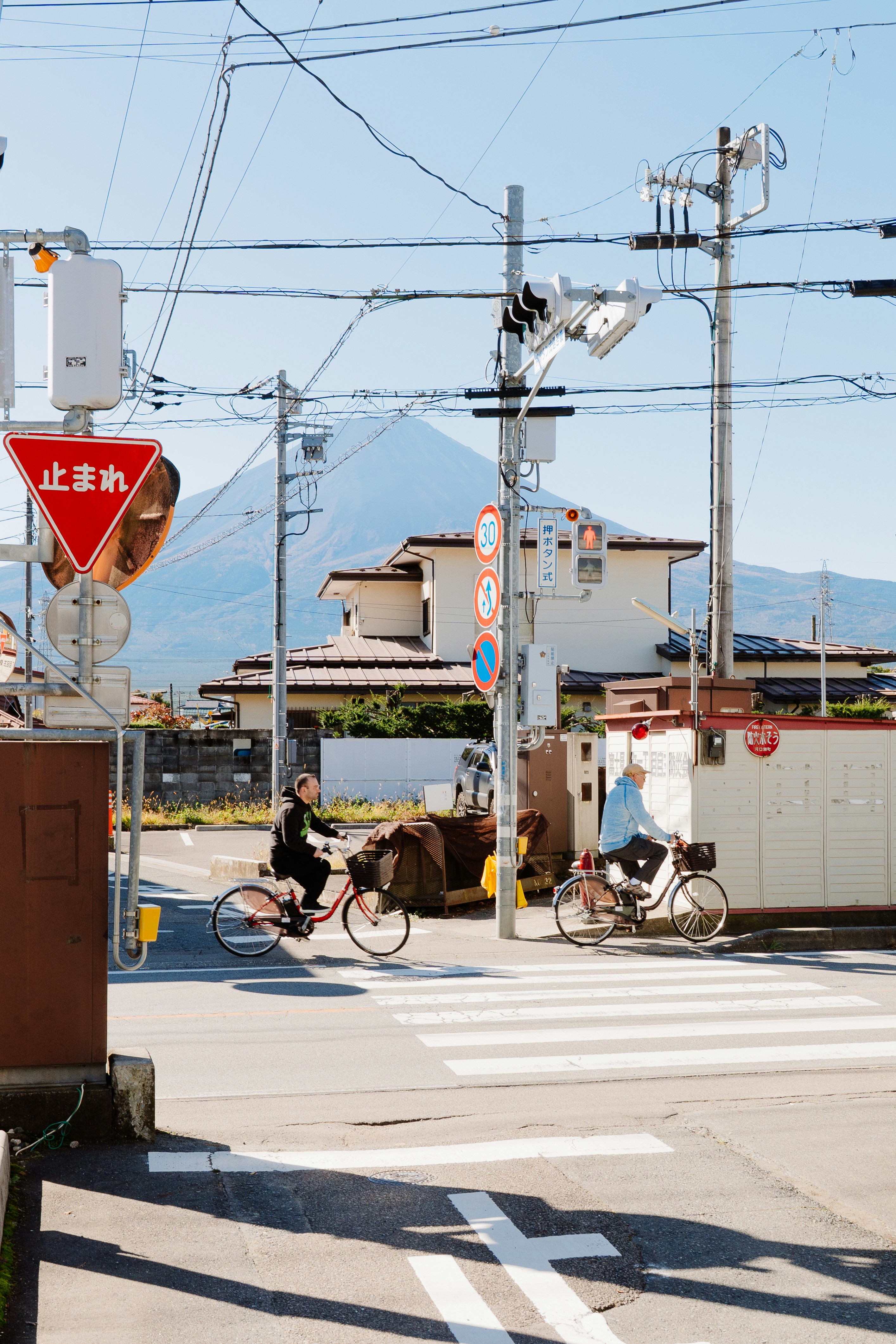 People on bicycles cross a street with mount fuji in view.