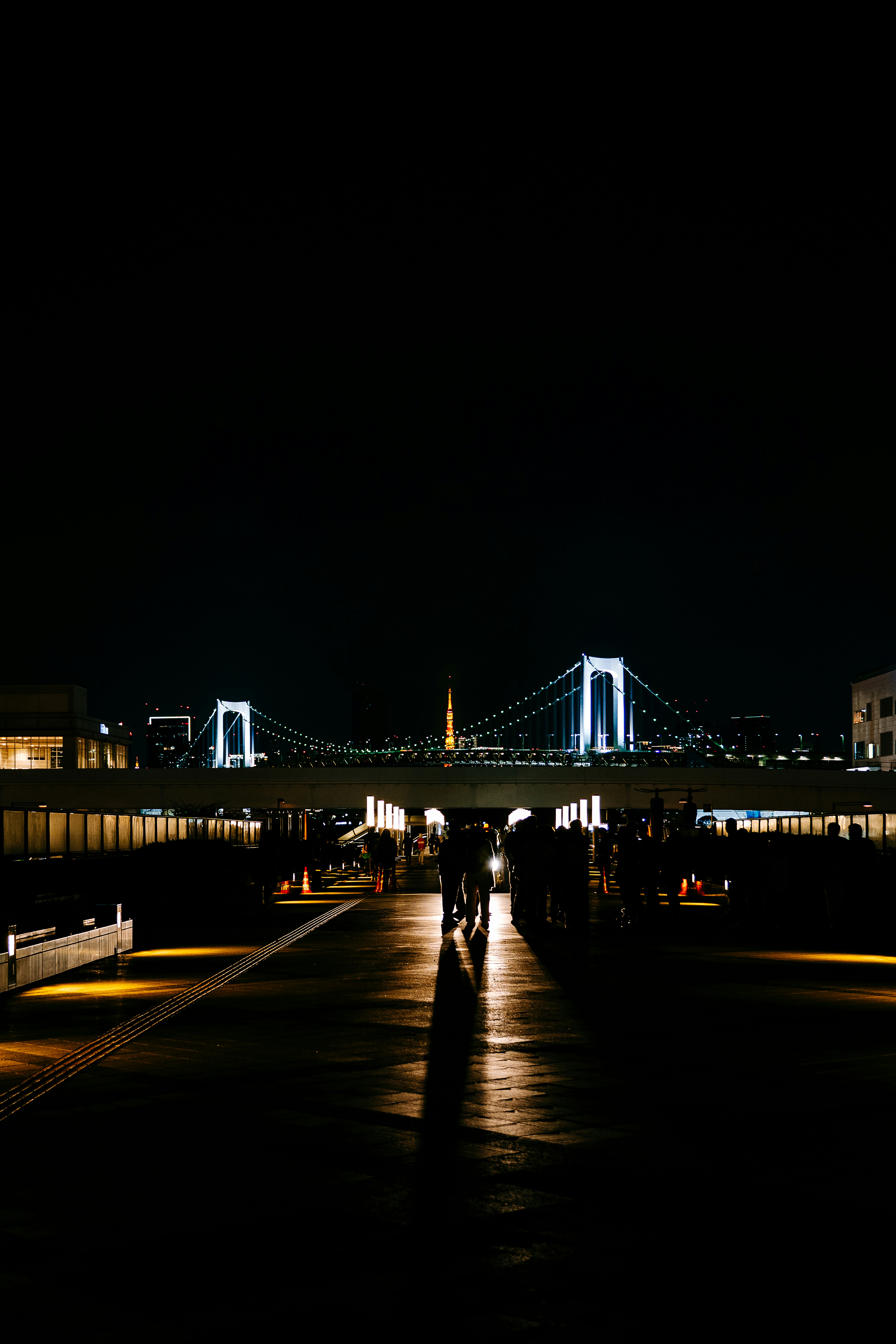 People walk toward a bridge at night.
