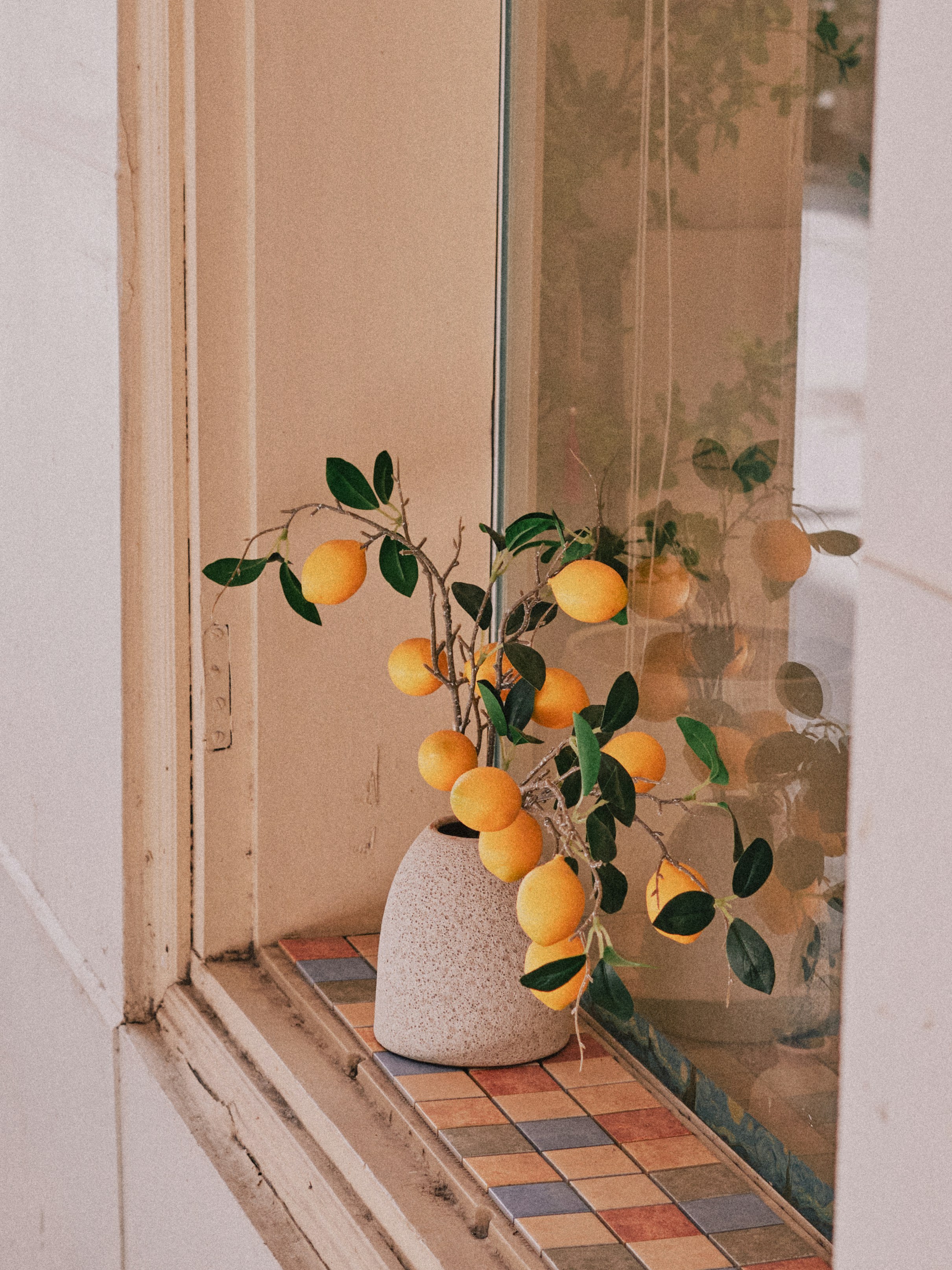 A quiet window whispers citrus dreams, where light lingers on golden fruit and tiled silence. | Lemons sit in a vase on a windowsill.