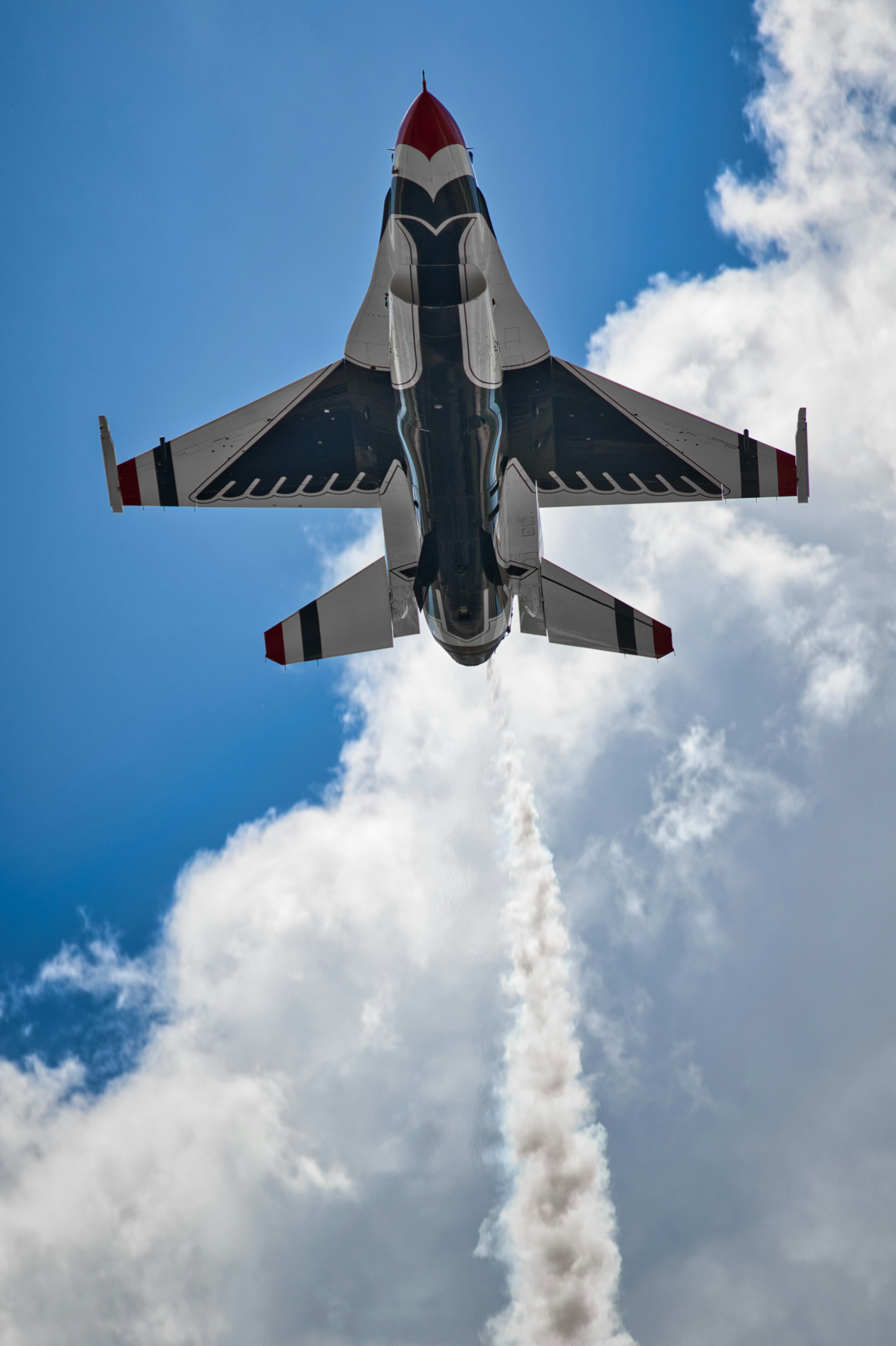 Fighter jet executing a vertical climb against a backdrop of blue sky and wispy clouds, leaving a trail of smoke behind.