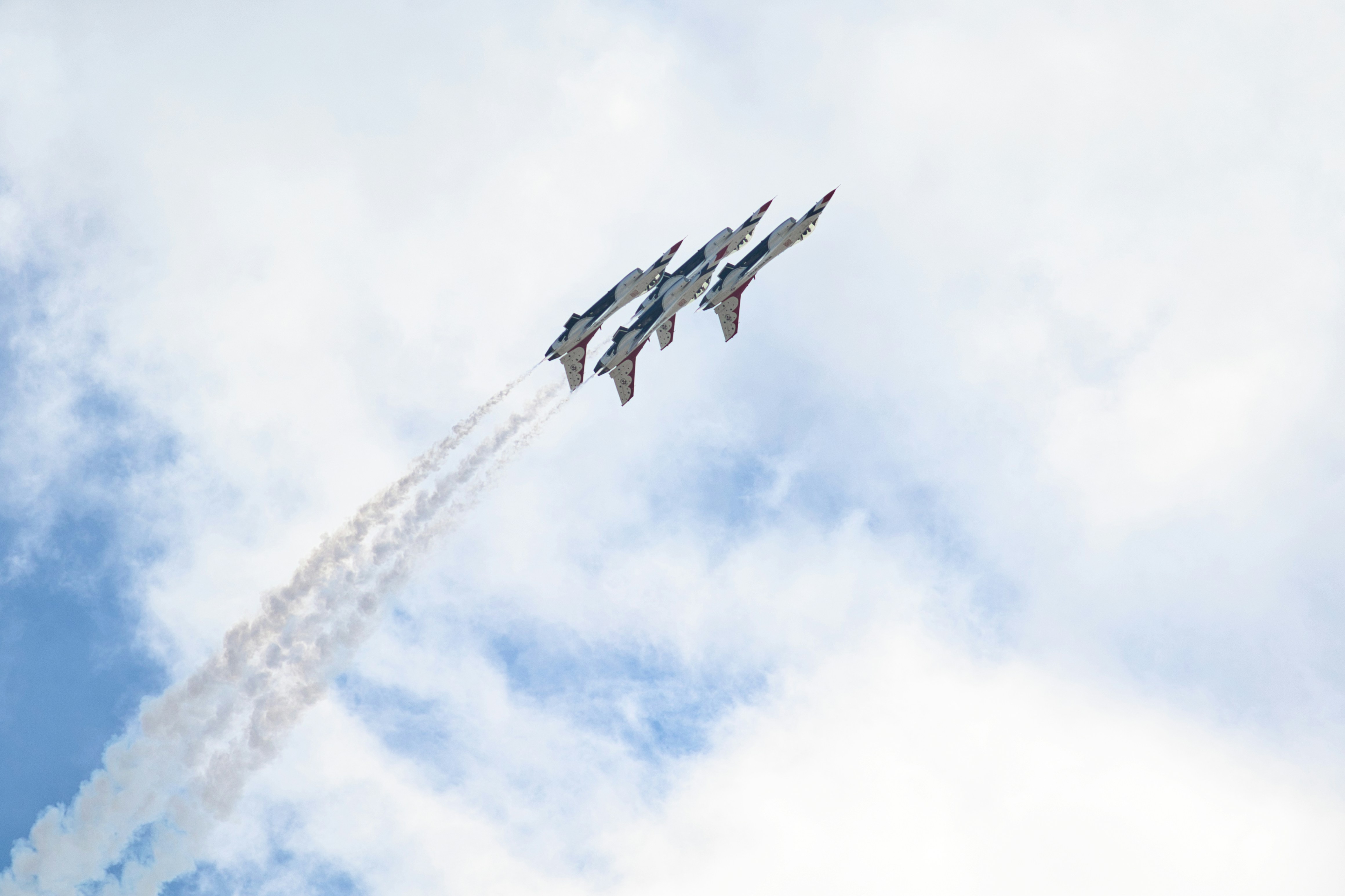 Three military jets performing a synchronized maneuver against a backdrop of fluffy clouds.