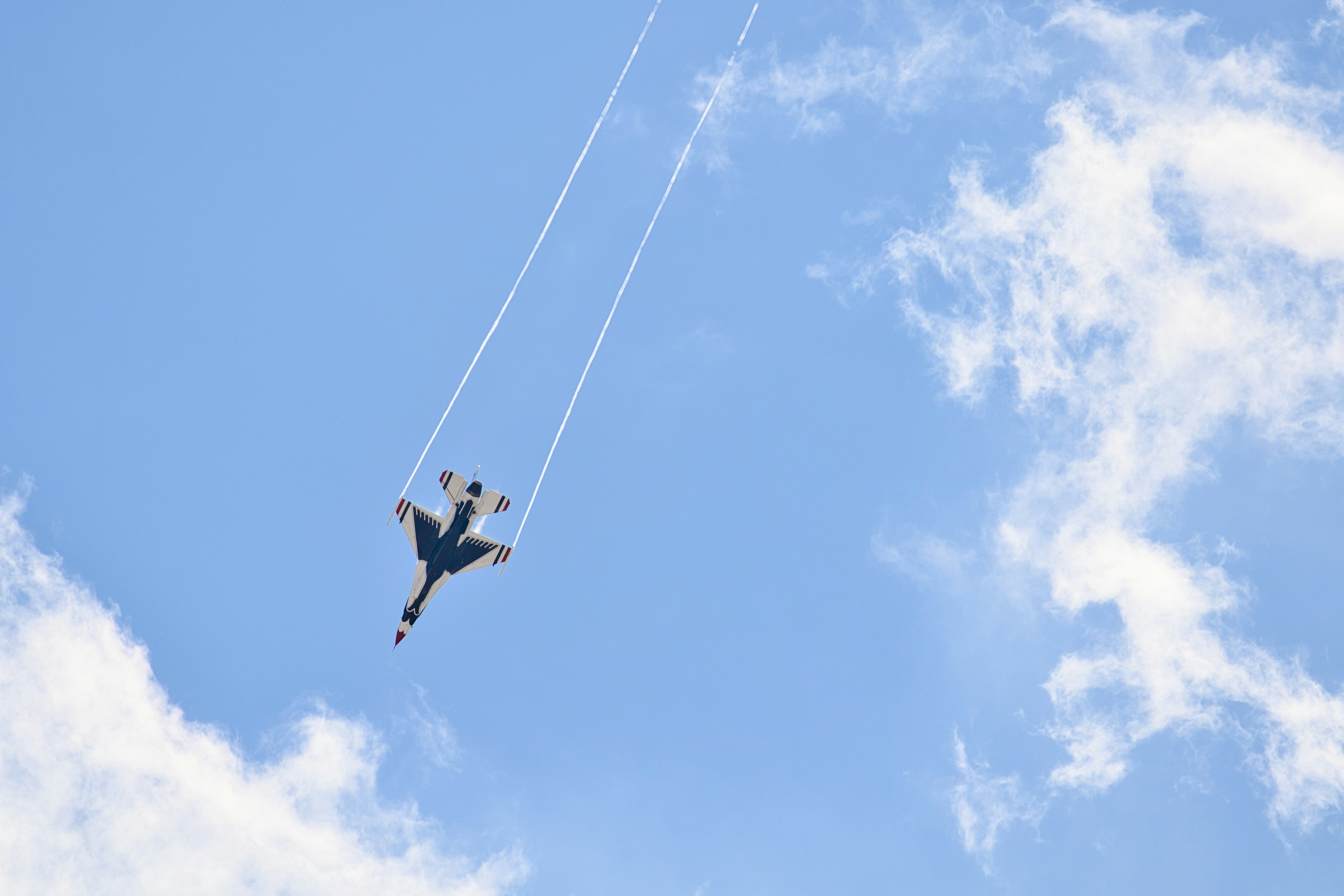 Thunderbirds | Jet fighter streaks across a bright, cloudy sky.
