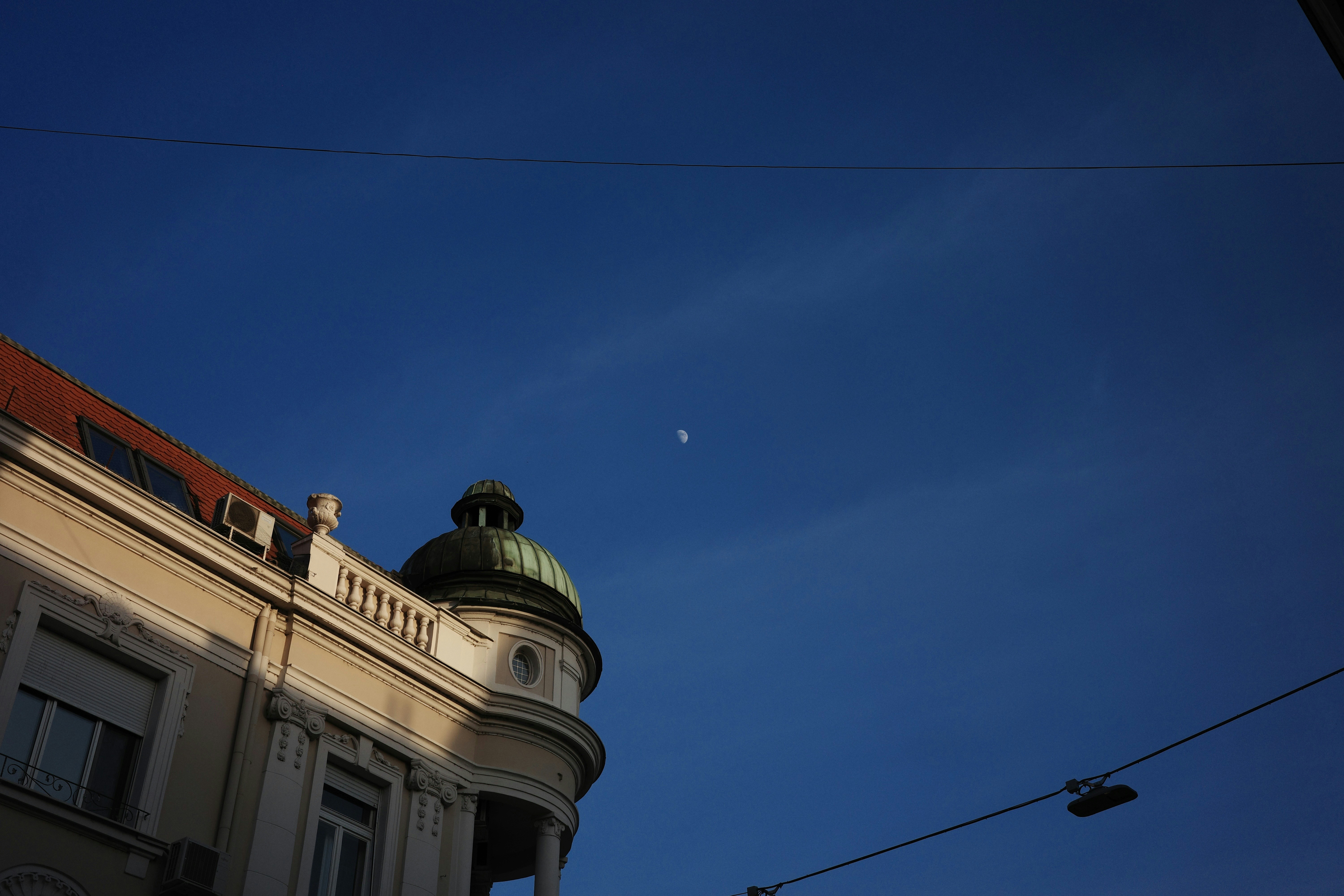 A historic building with a green dome under a clear blue sky, featuring a crescent moon in the background.