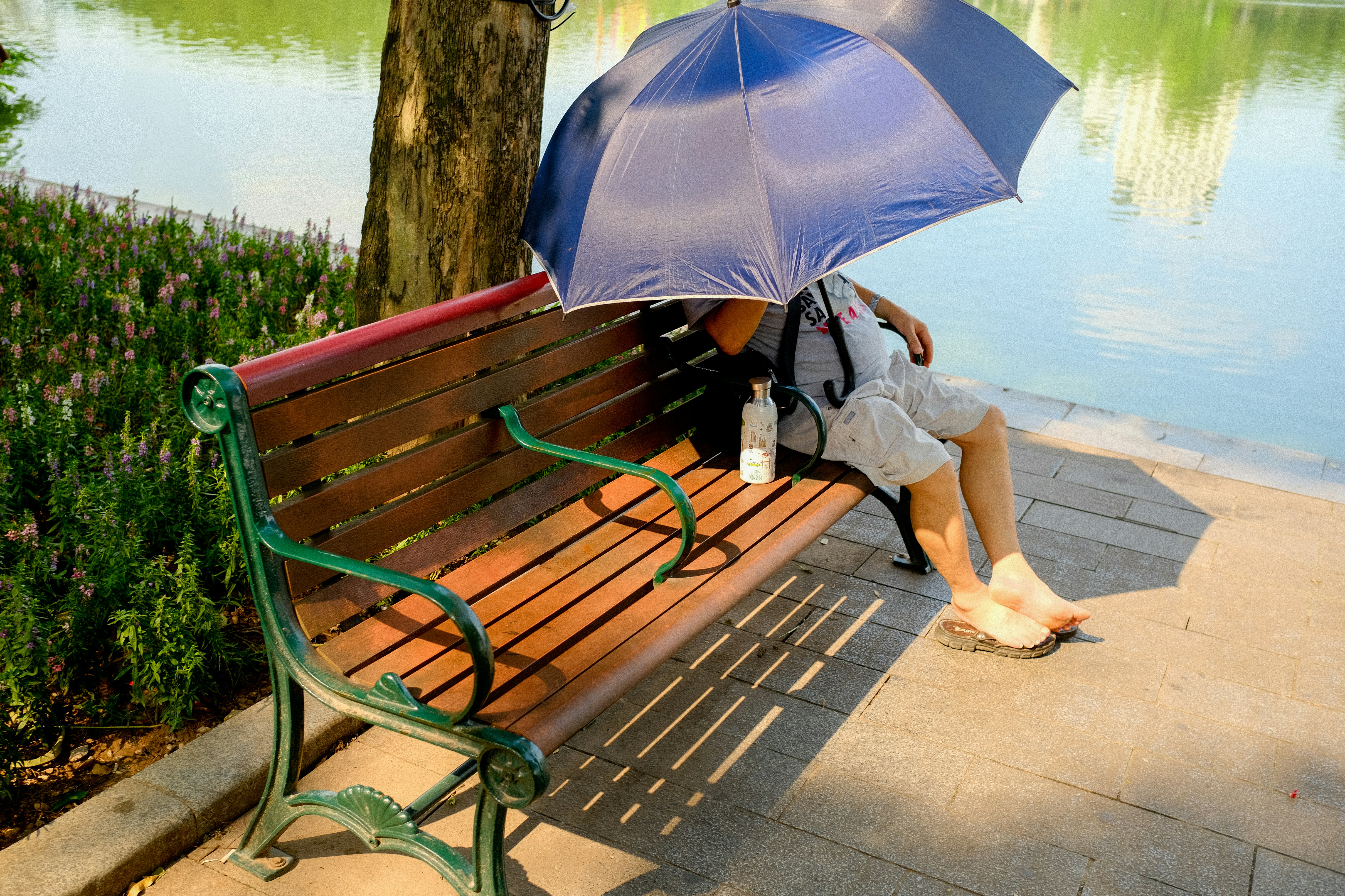 Person rests on a bench, shaded by an umbrella.