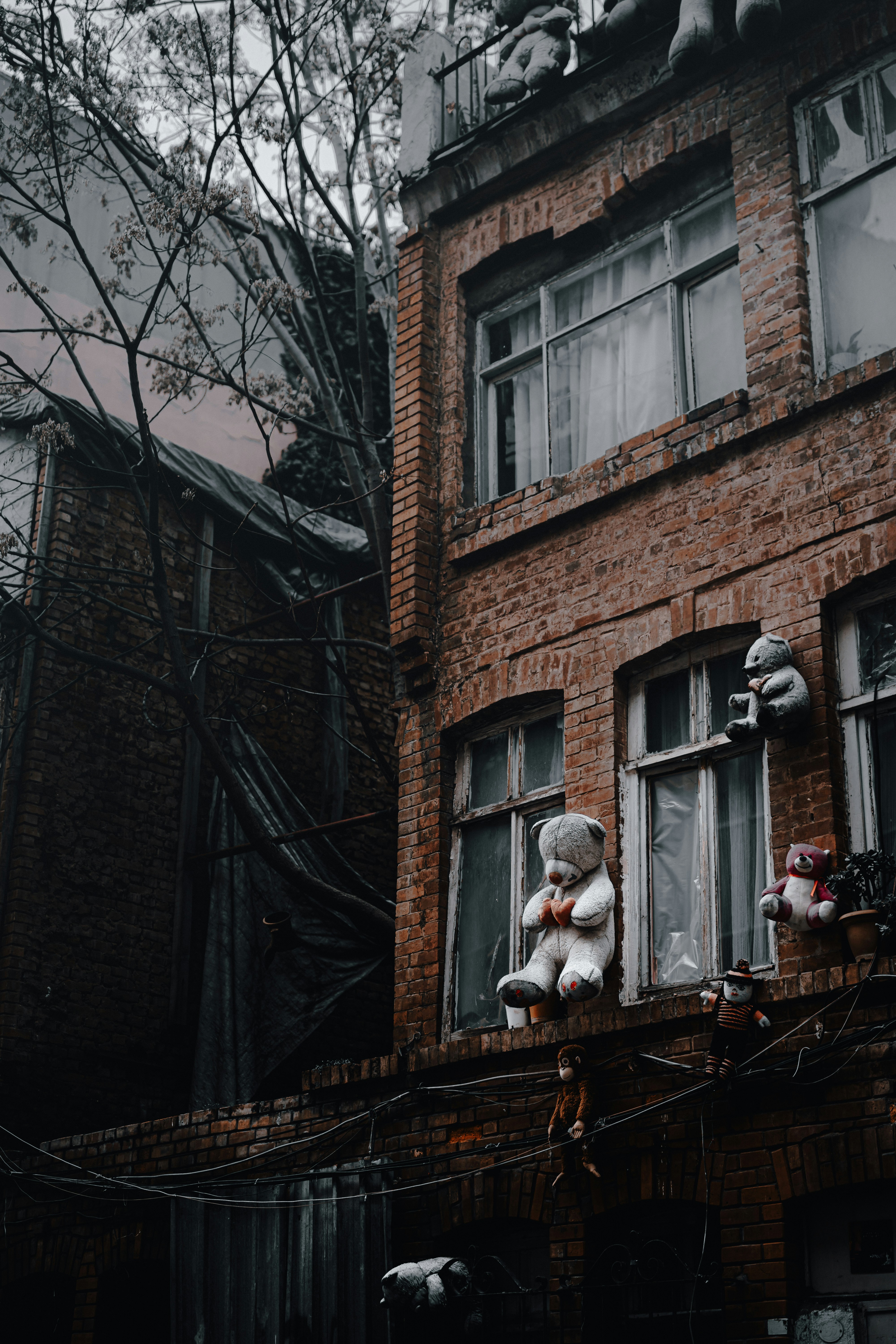 A weathered brick building adorned with plush toys, creating a surreal contrast against its gritty surroundings. The scene evokes a sense of nostalgia and whimsy.