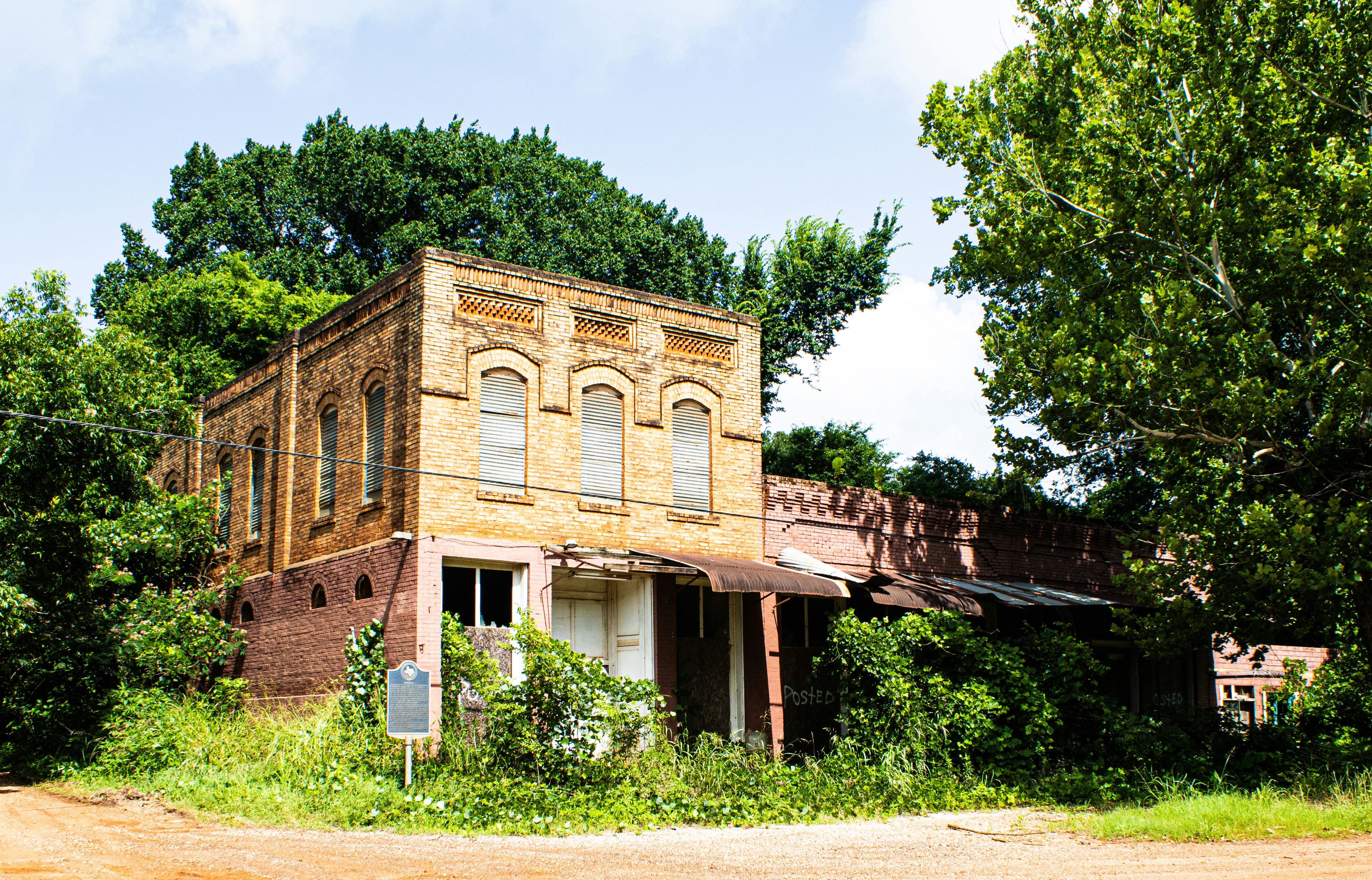 Abandoned downtown Dialville, TX | Old, brick building sits surrounded by green foliage.