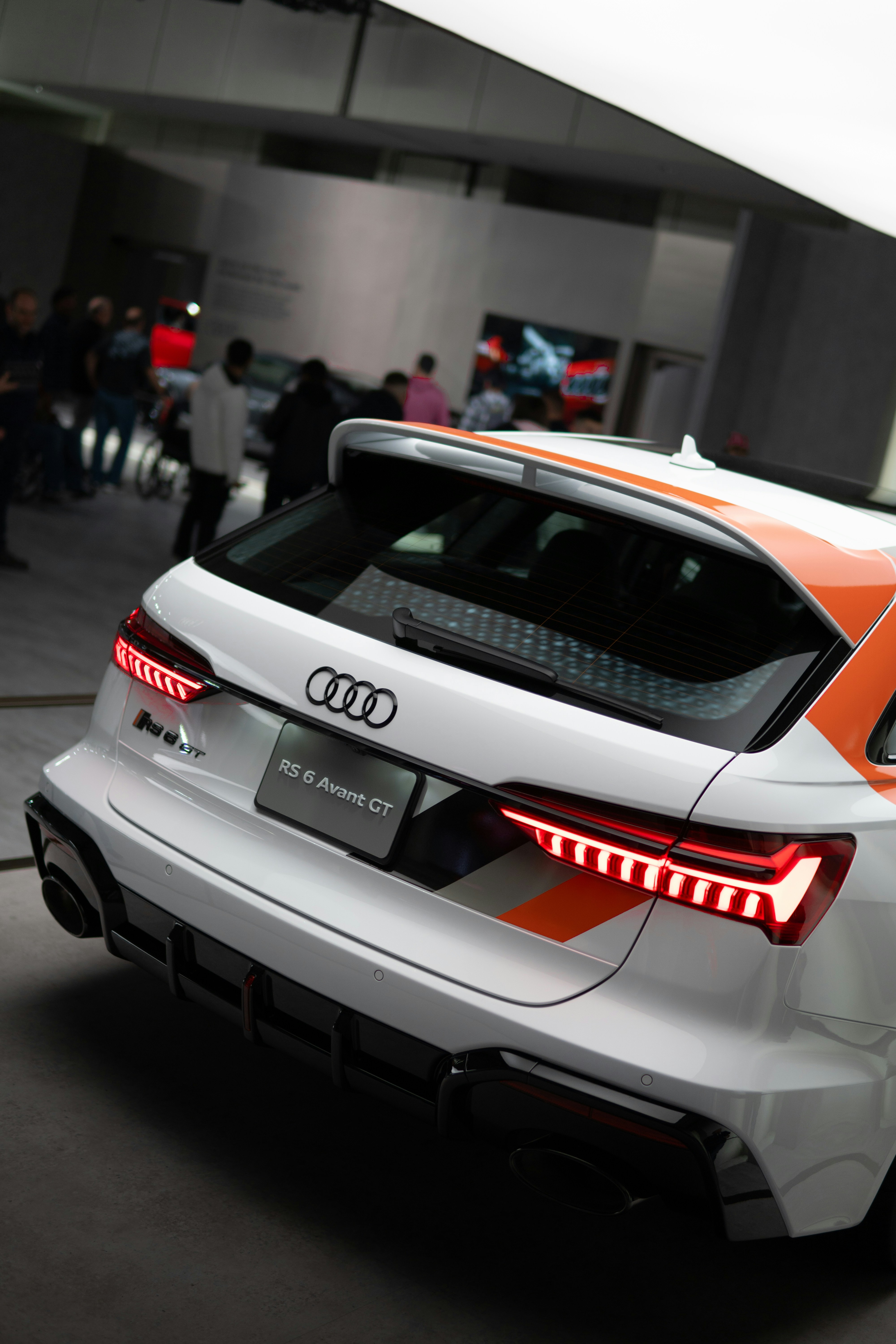 Showroom Spotlight on an Audi RS 6 Avant GT: White body, orange accents, and a crowd in the background