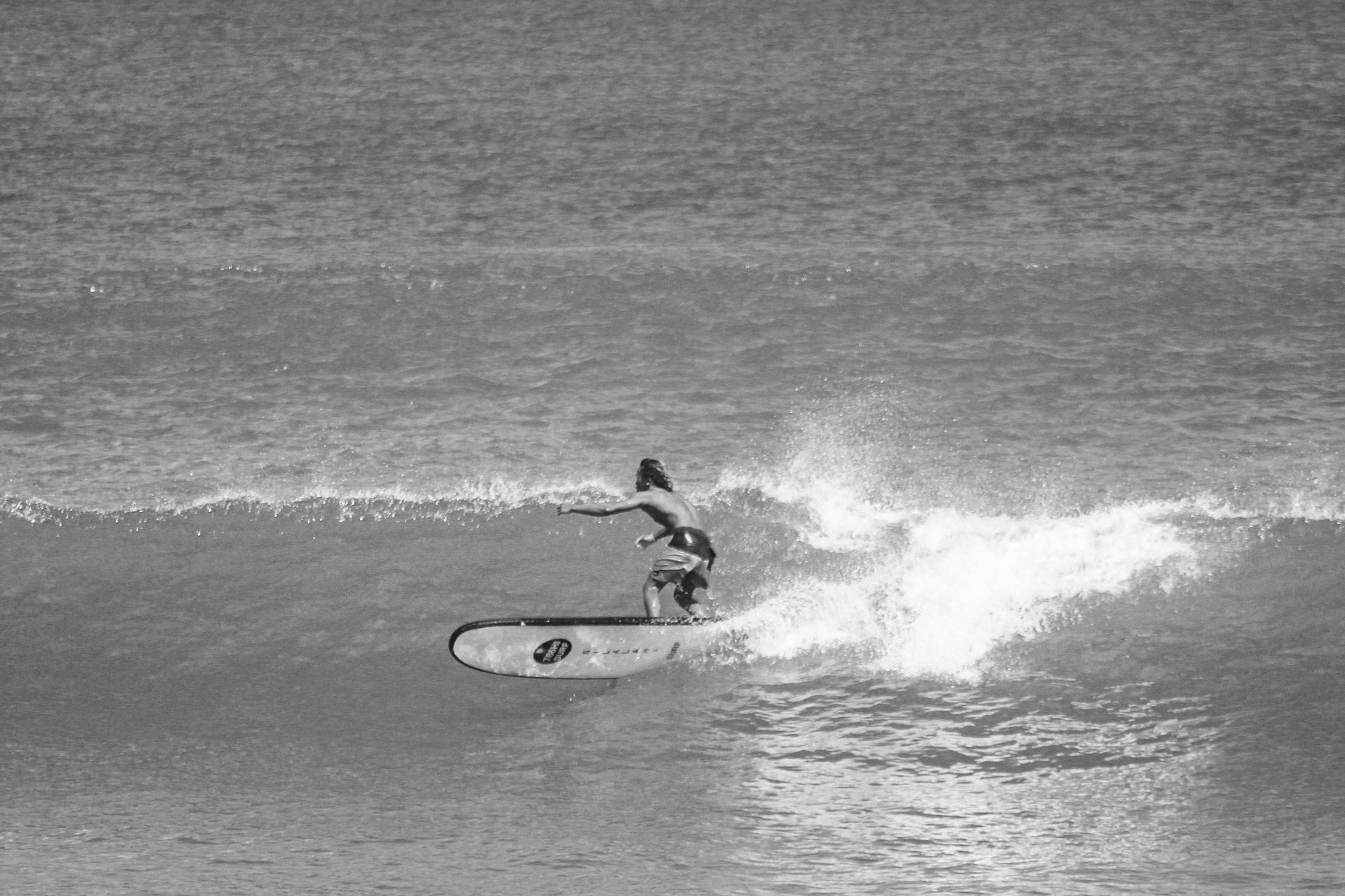 A surfer rides a wave in black and white.