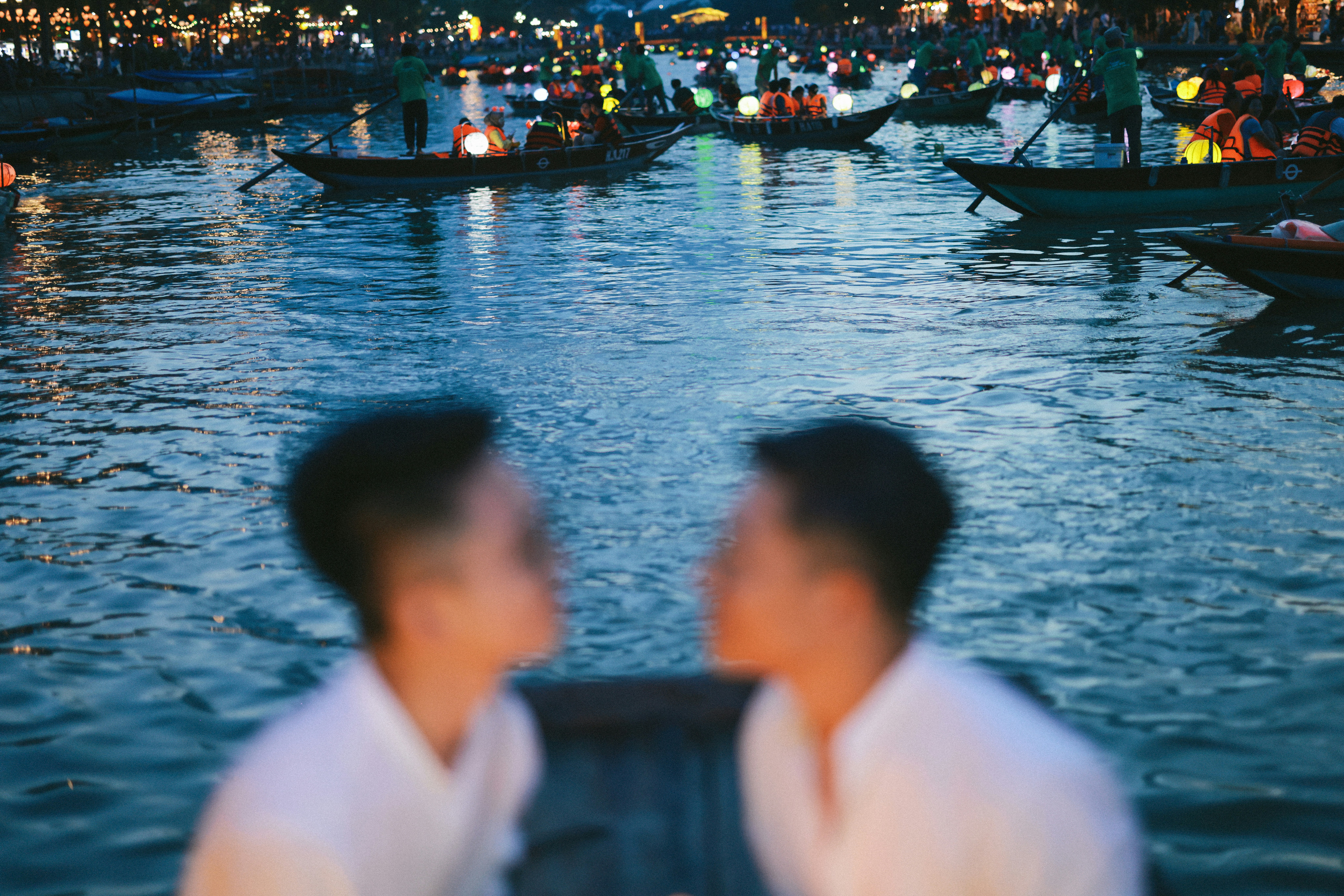 Two figures share an intimate moment on a boat, with colorful lanterns illuminating the water and other boats in the background.