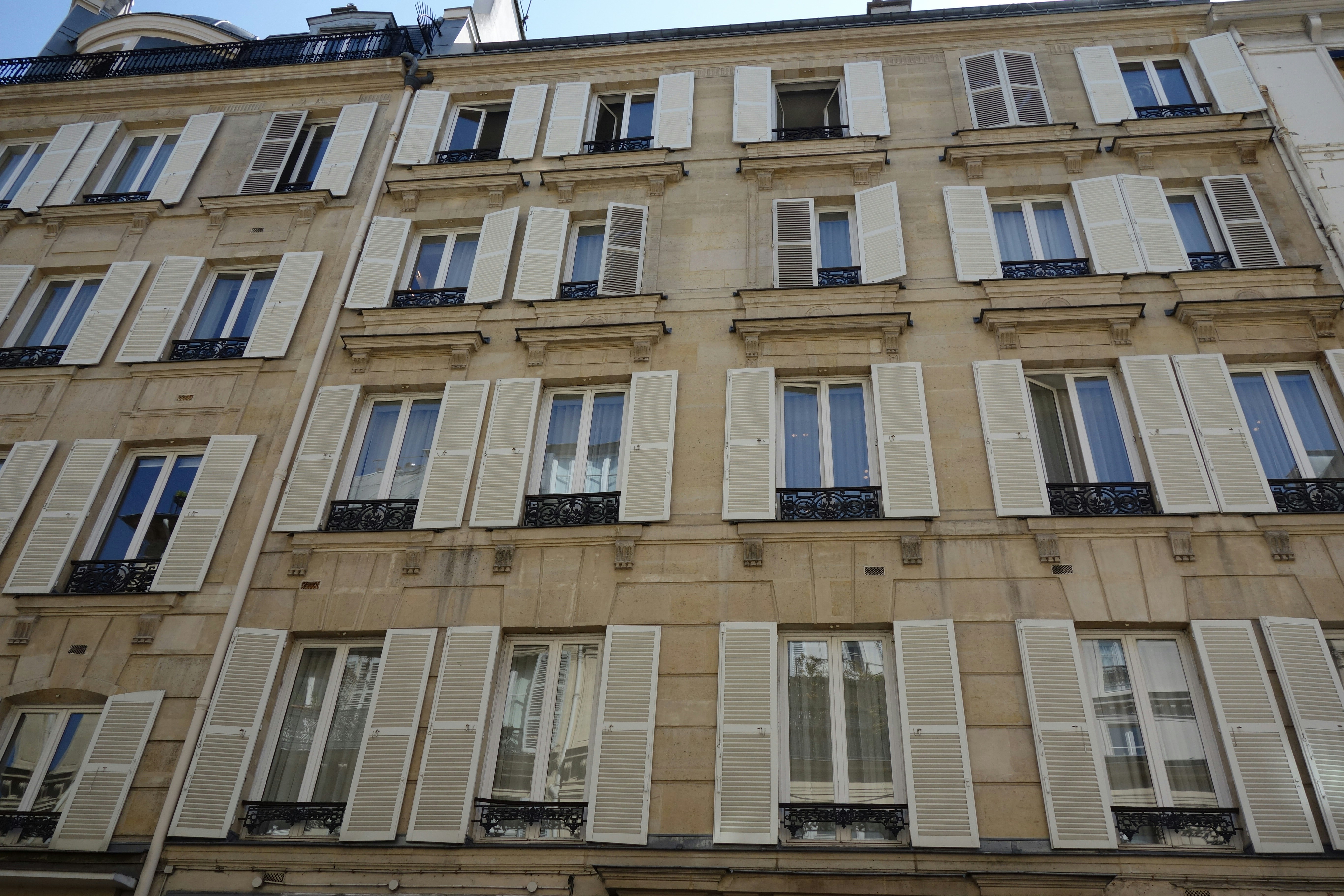 A charming Parisian building facade adorned with classic white shutters and intricate wrought iron balconies, showcasing the elegance of urban living.