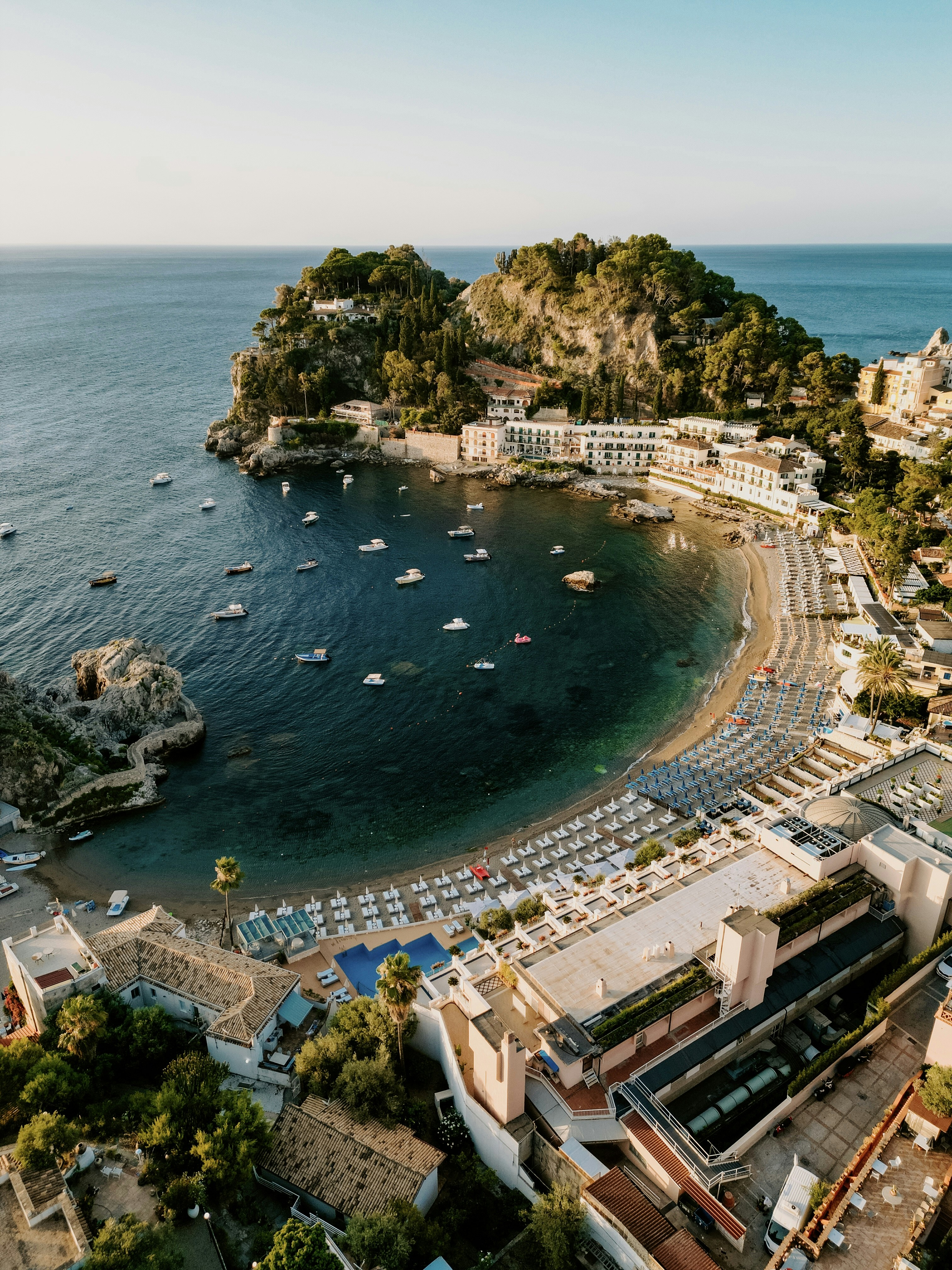 Aerial view of a tranquil cove surrounded by lush greenery and a charming resort, with boats gently floating on the calm waters. The scene captures the essence of relaxation and natural beauty.