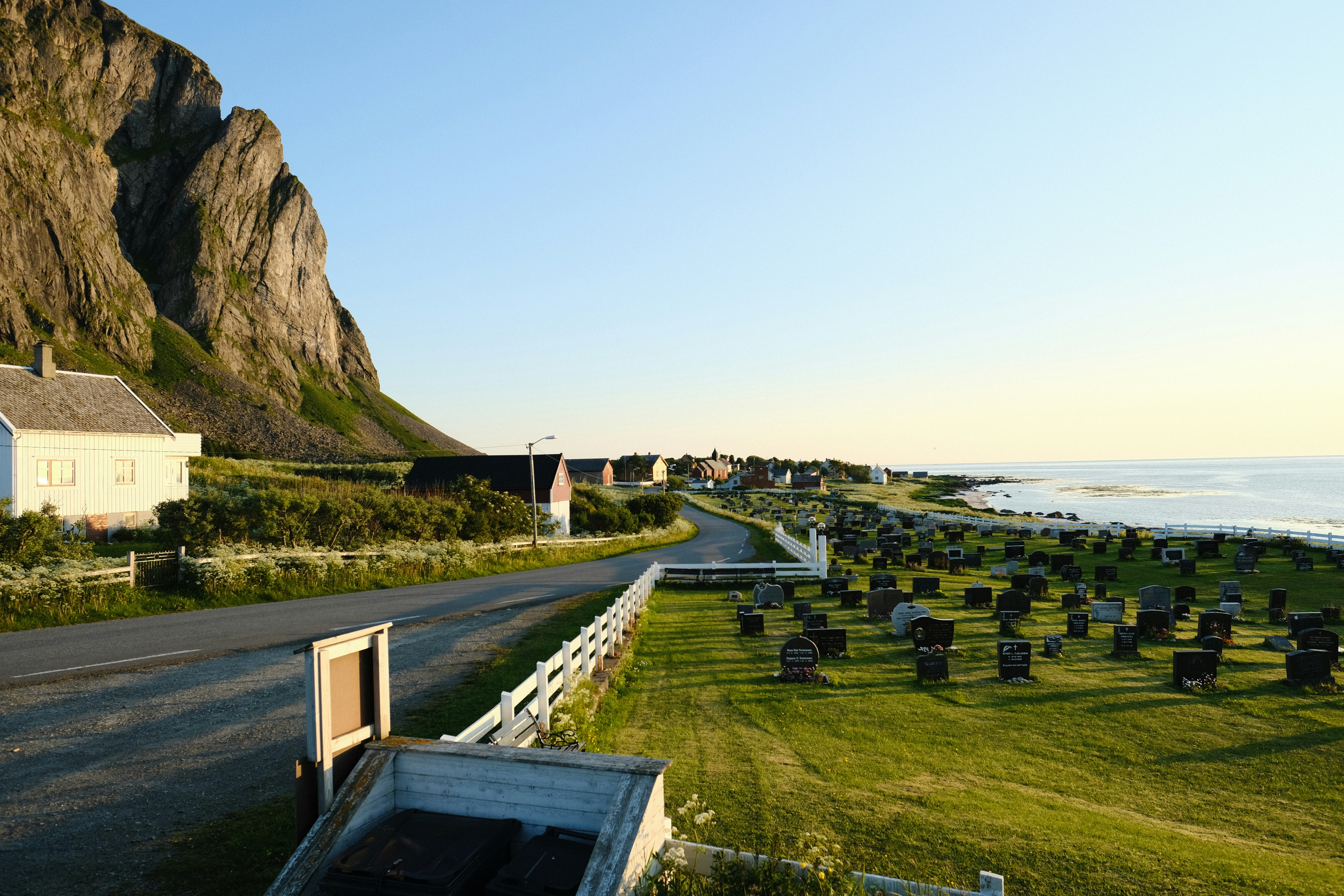 Midnight sun hitting the Værøy kirkegård. | Coastal village with cemetery and mountain.