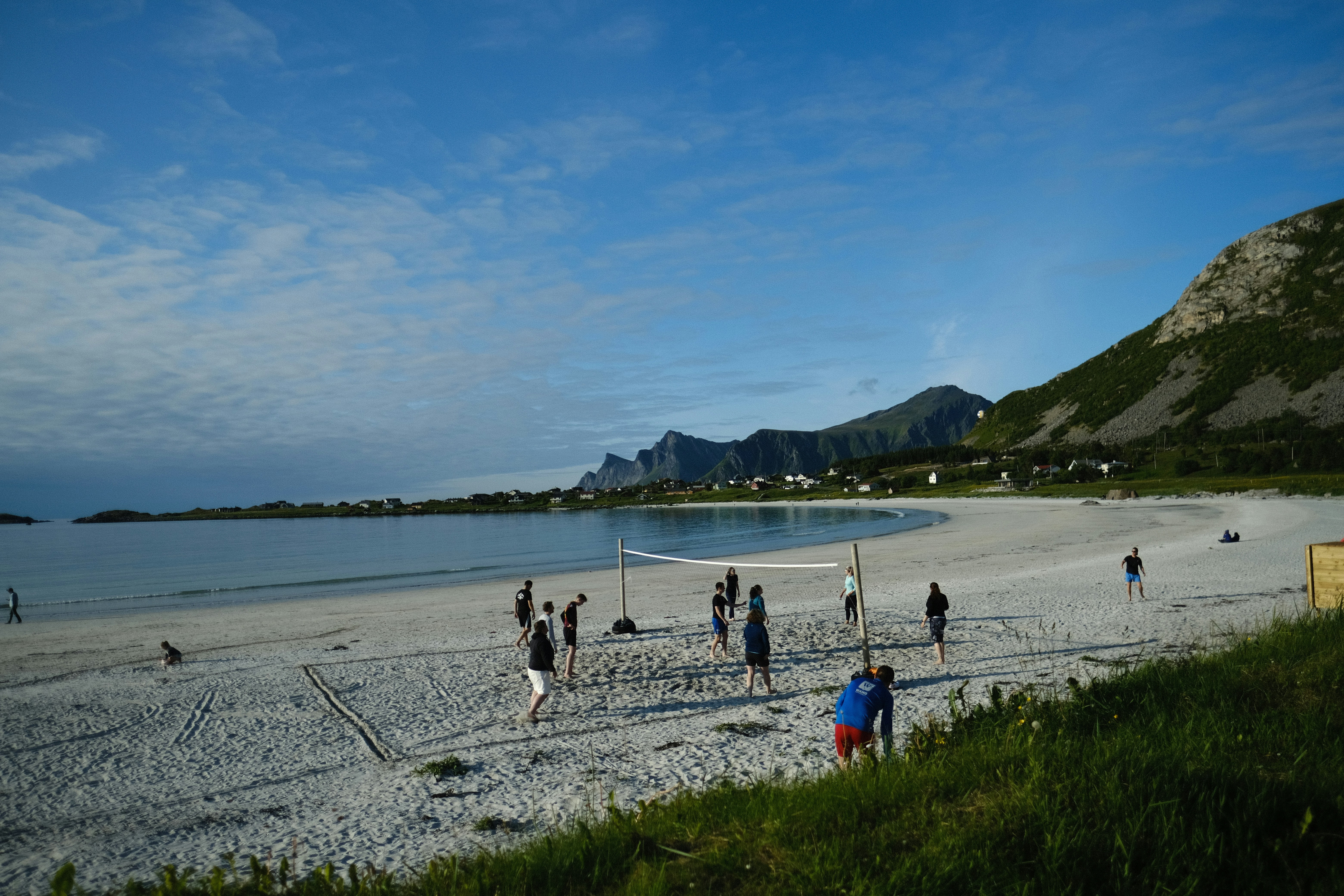 People playing beach volleyball on a scenic beach. | People are playing volleyball on a beautiful beach.