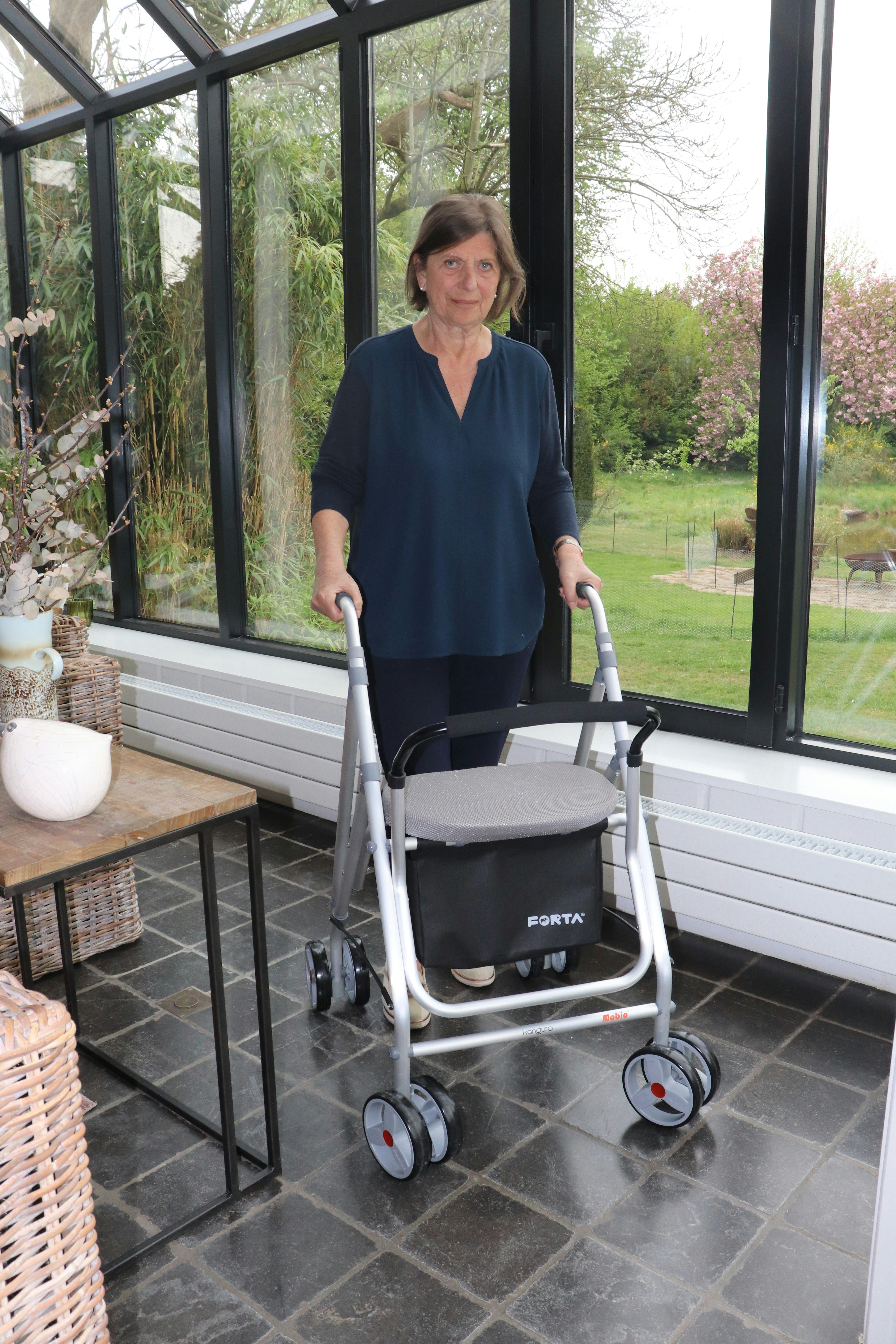 Woman using a walking aid rollator | Woman uses a walker in a bright sunroom.