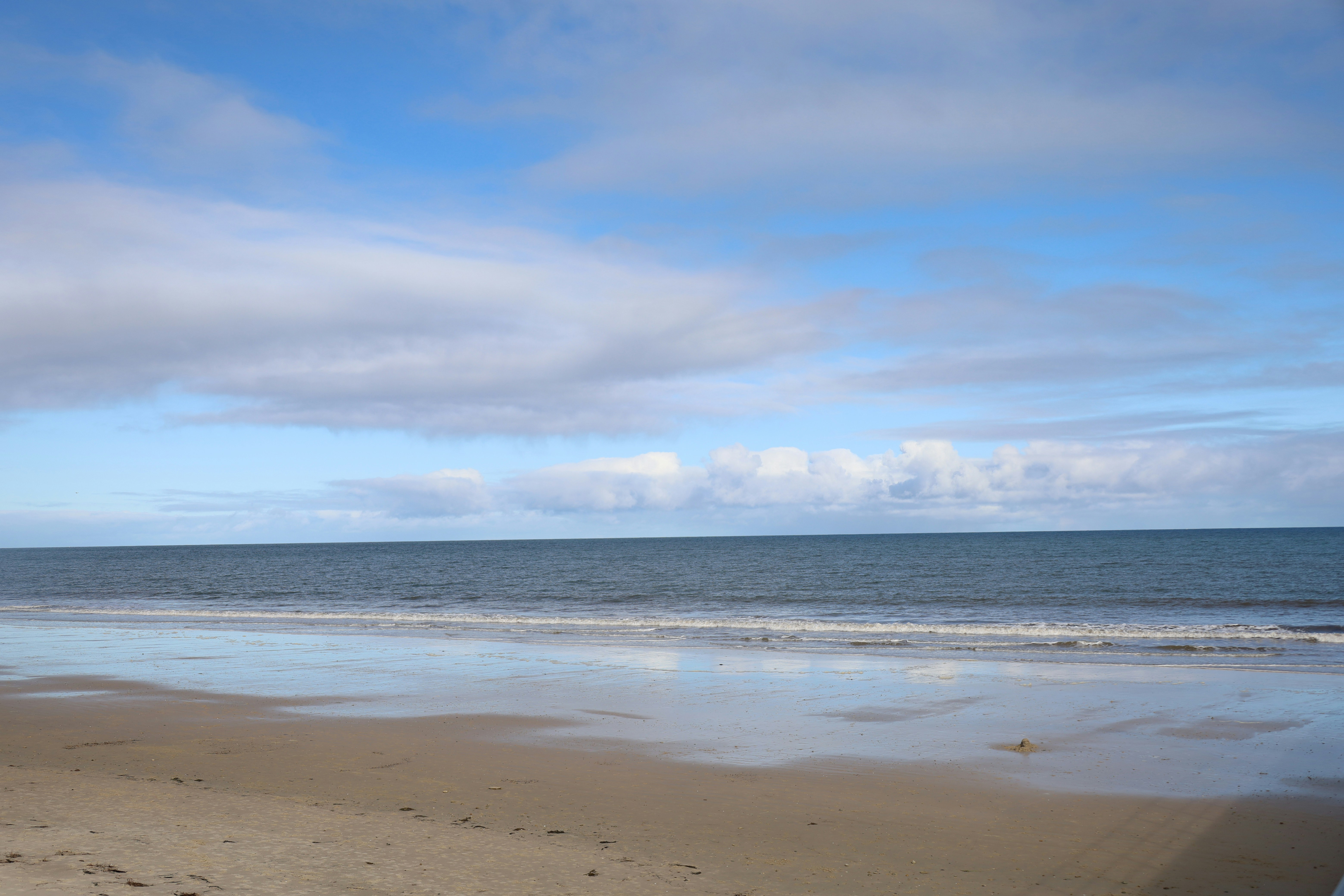 Beach meets the ocean under a cloudy sky.