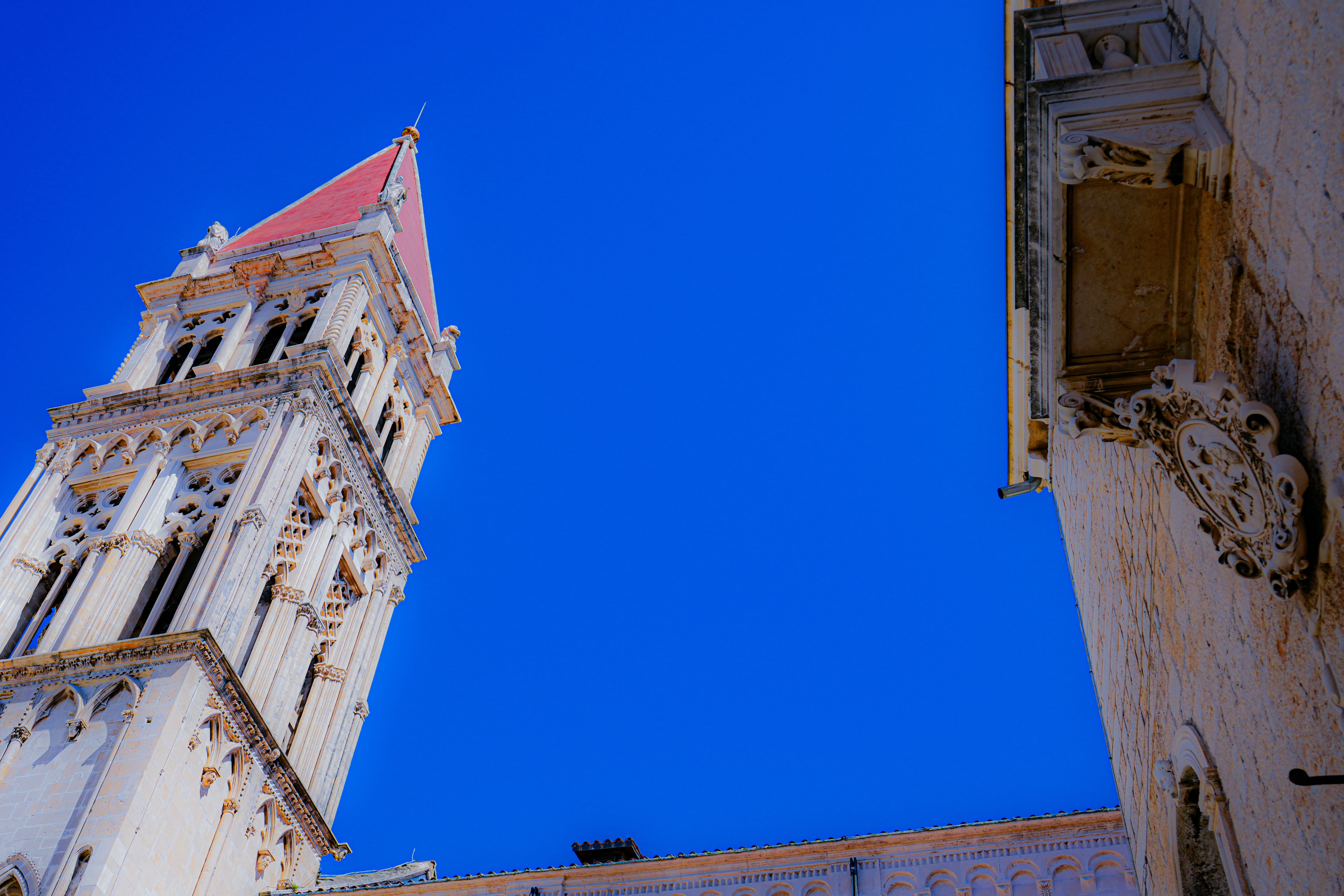 Historic bell tower rising against a vibrant blue sky, showcasing intricate architectural details and a striking red roof.