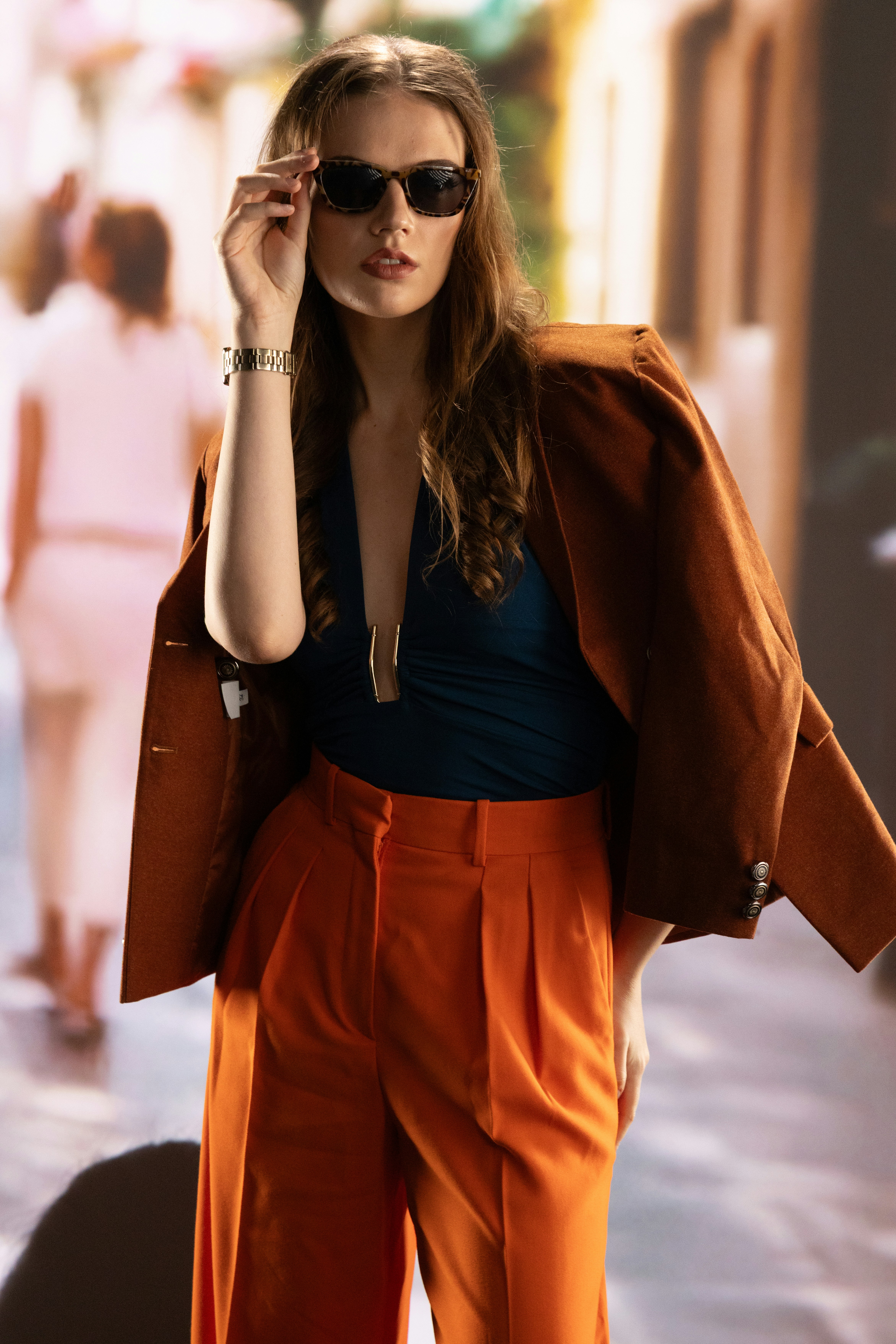 Woman in stylish outfit adjusts sunglasses.