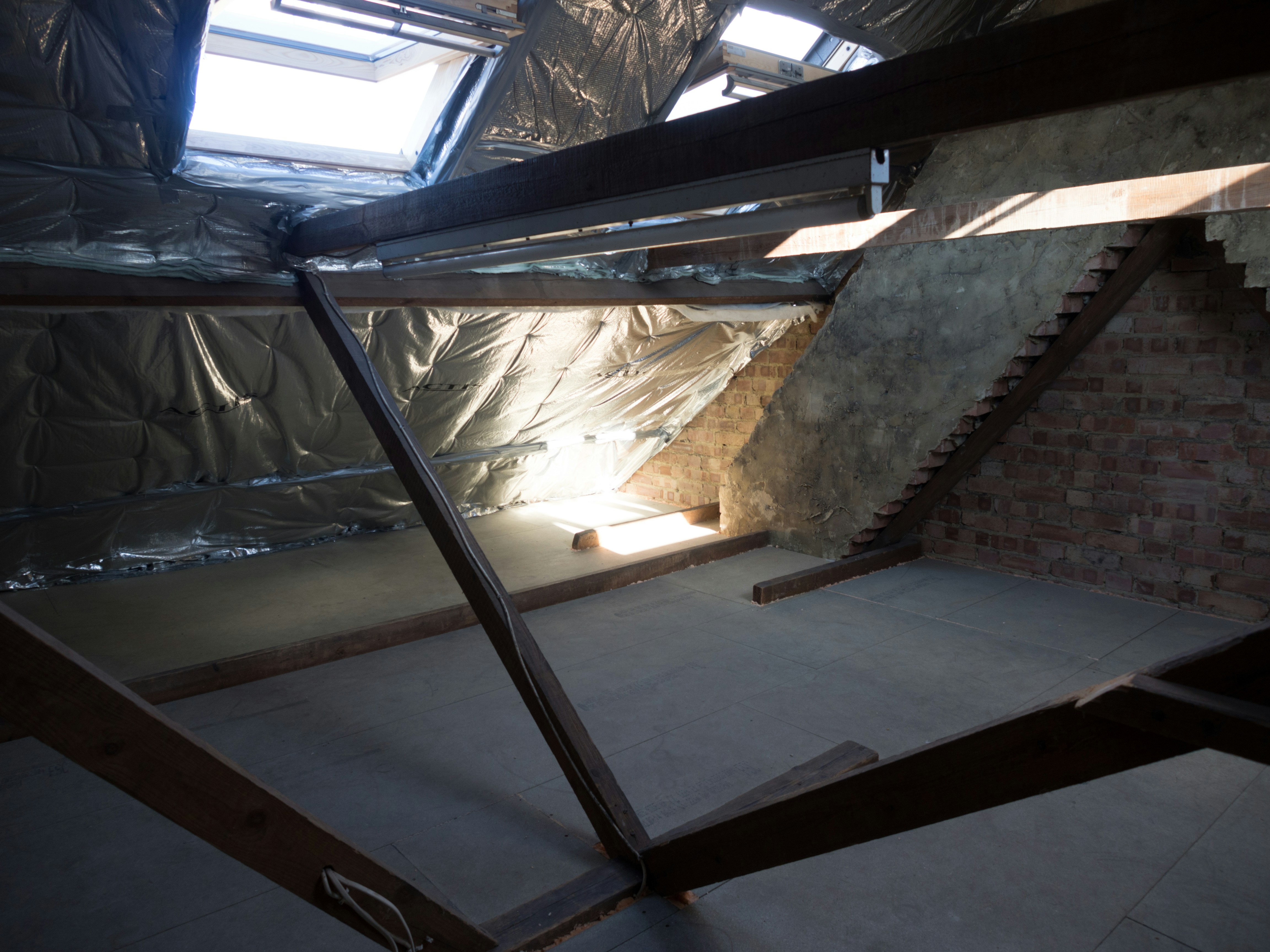 Bright attic space with exposed wooden beams and skylights, showcasing a blend of raw materials and natural light.