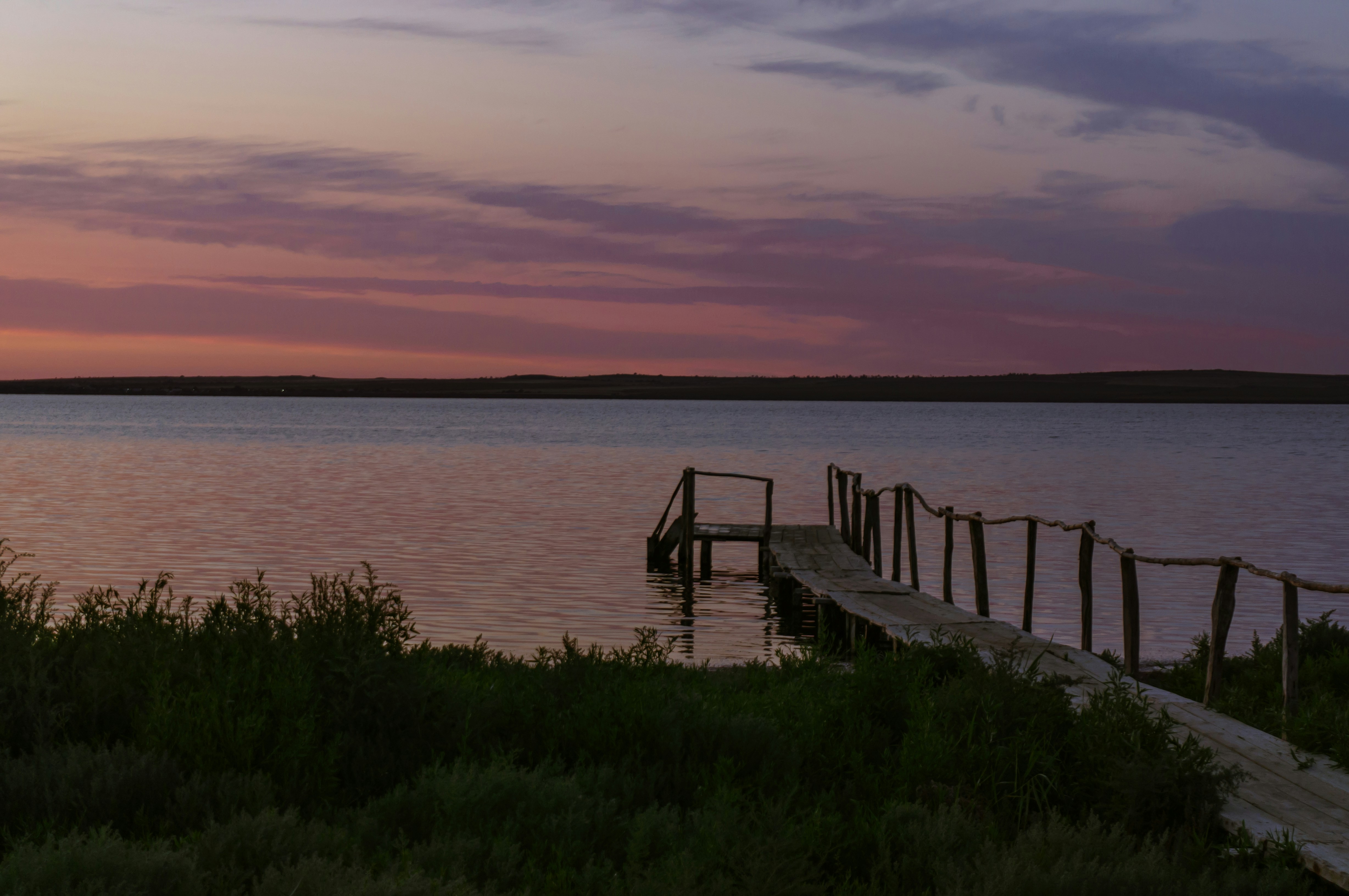A wooden dock extends into peaceful waters at sunset.