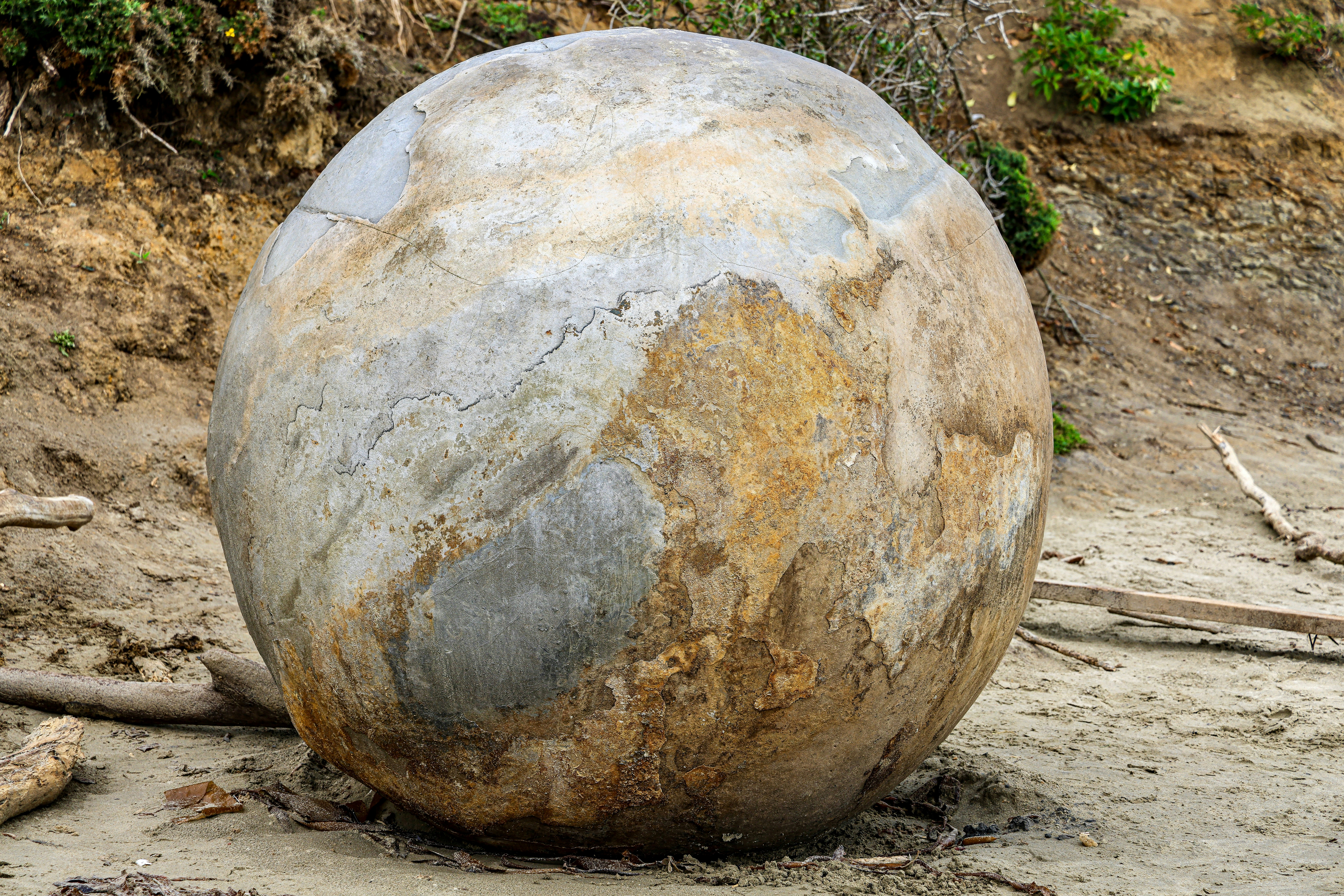 A large, round boulder sits on sandy ground.