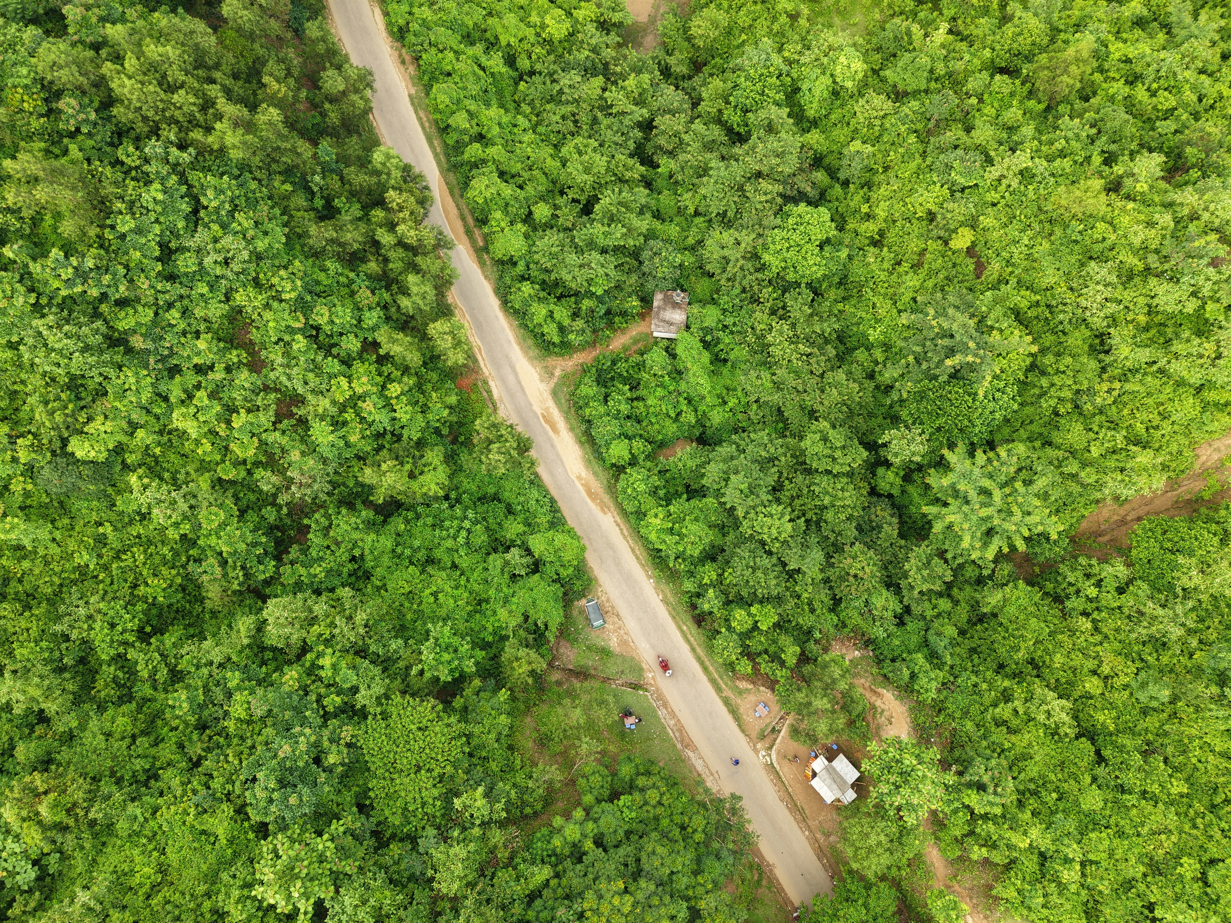 Winding Road Through Mini Bandarban, Cox’s Bazar An aerial view of a scenic winding road cutting through dense green forest in the Mini Bandarban area of Inani Beach, Cox’s Bazar, Bangladesh. Captured with a DJI Air 3S, this drone photo beautifully showcases the untouched greenery, rural tranquility, and the quiet charm of a hidden gem often called “Mini Bandarban” due to its hilly terrain and natural beauty. Perfect for themes of nature exploration, forest conservation, adventure travel, and remote landscapes. | An aerial view shows a road through lush greenery.