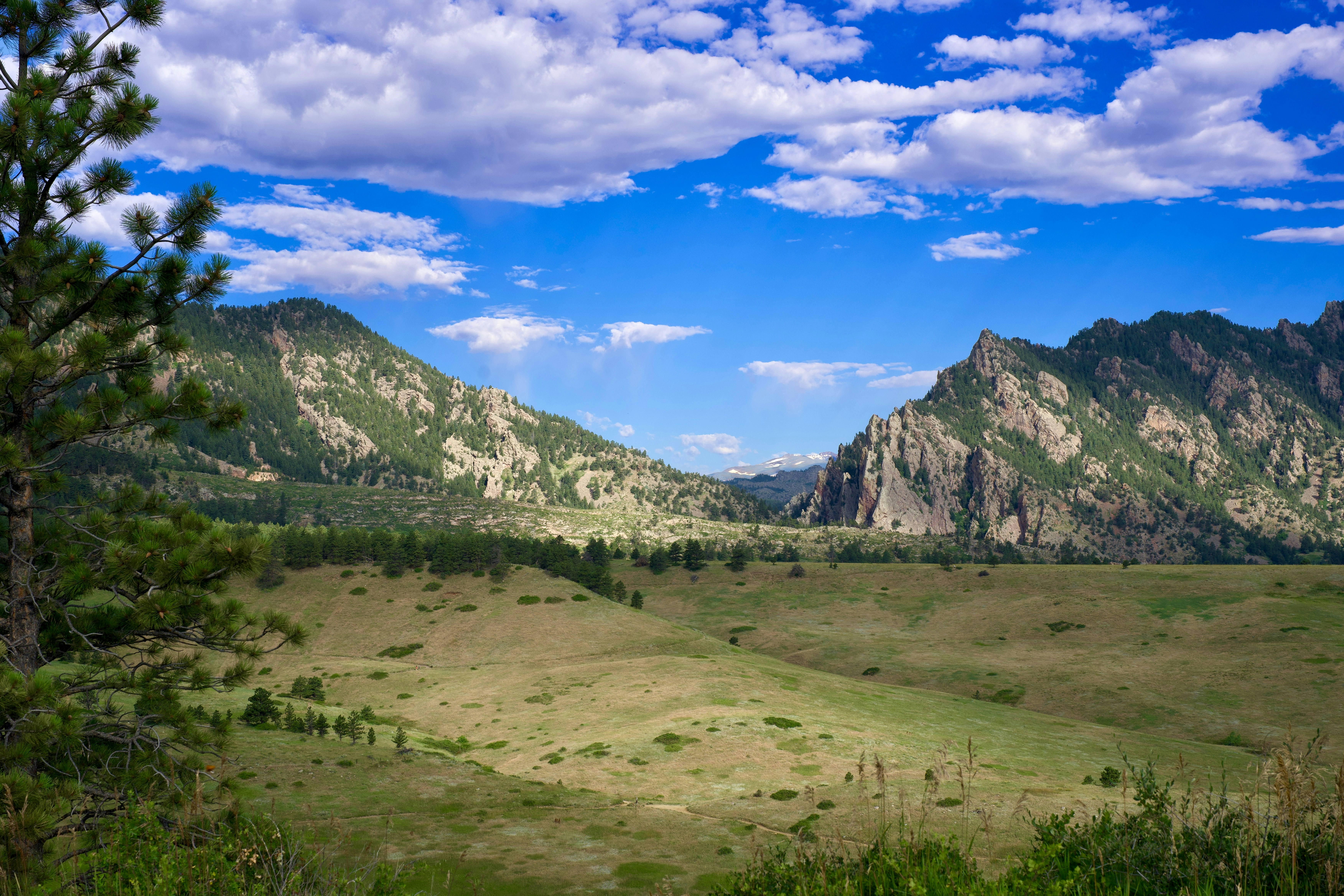 Vast open meadow framed by majestic rocky mountains under a vibrant sky with scattered clouds.