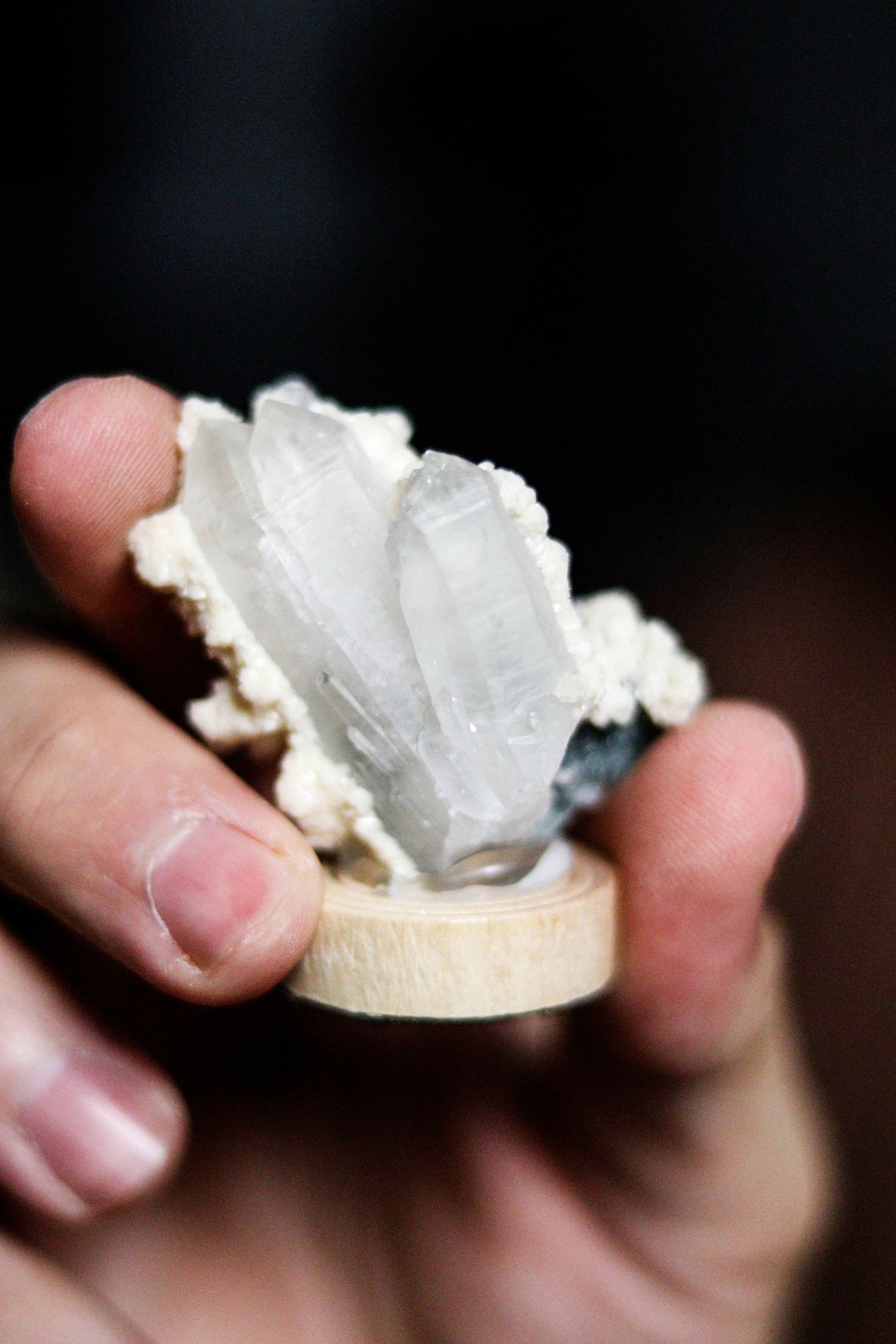 Hand holding a crystal cluster on a wooden base.