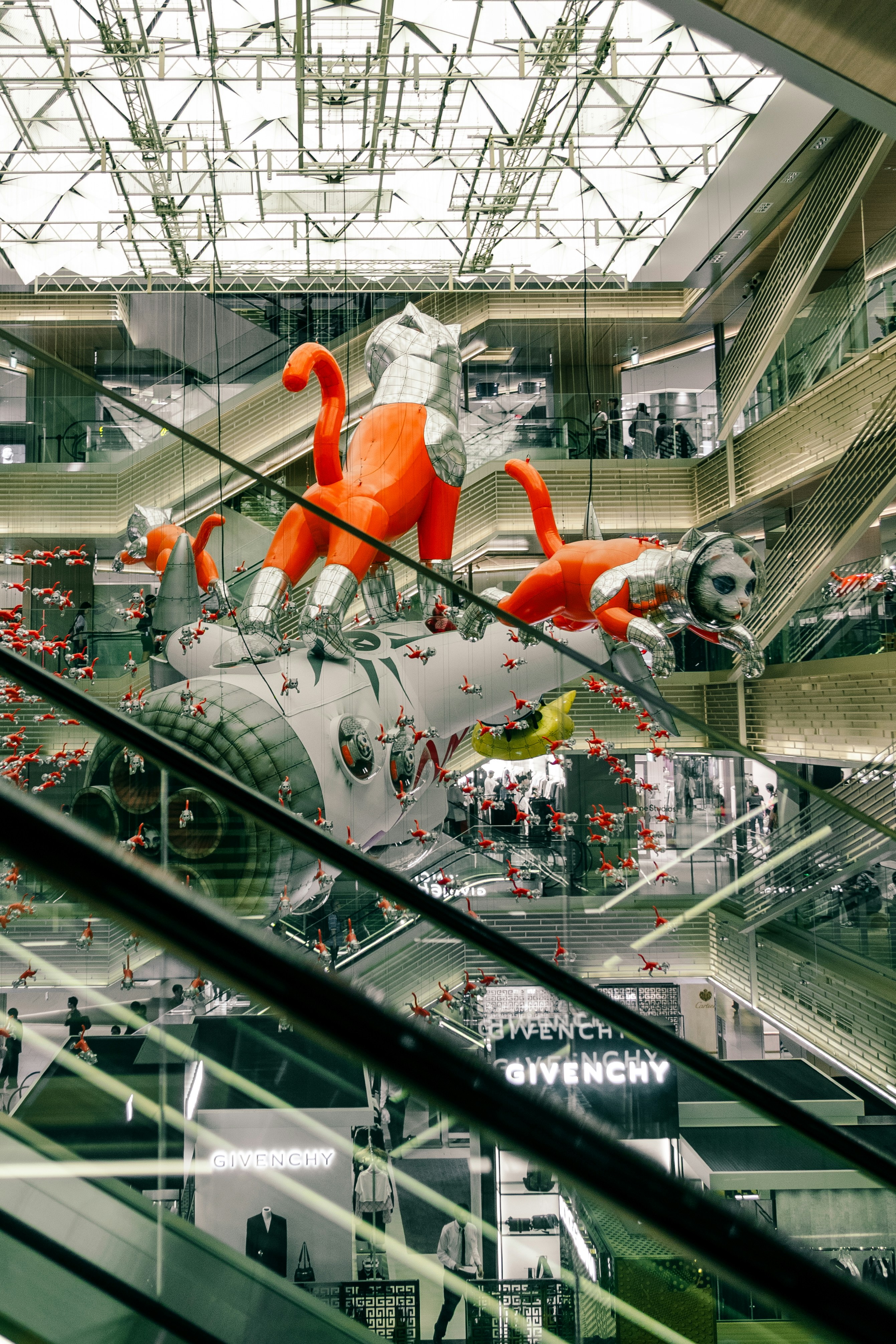 Hovering Orange Figures Over a Glass Atrium: A Fashion Mall Installation