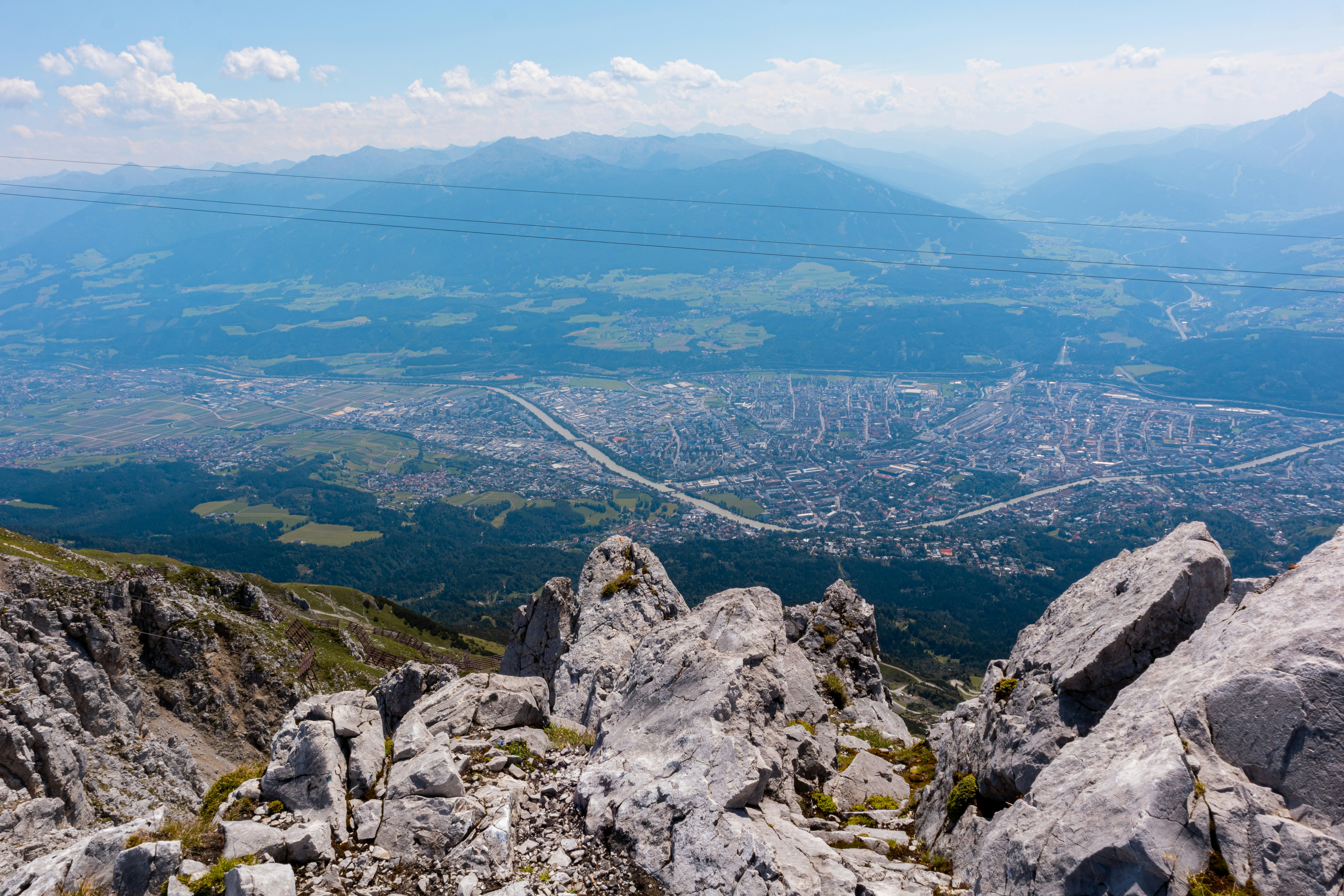 Rocky mountain summit overlooking a sprawling valley and distant mountains under a clear blue sky.
