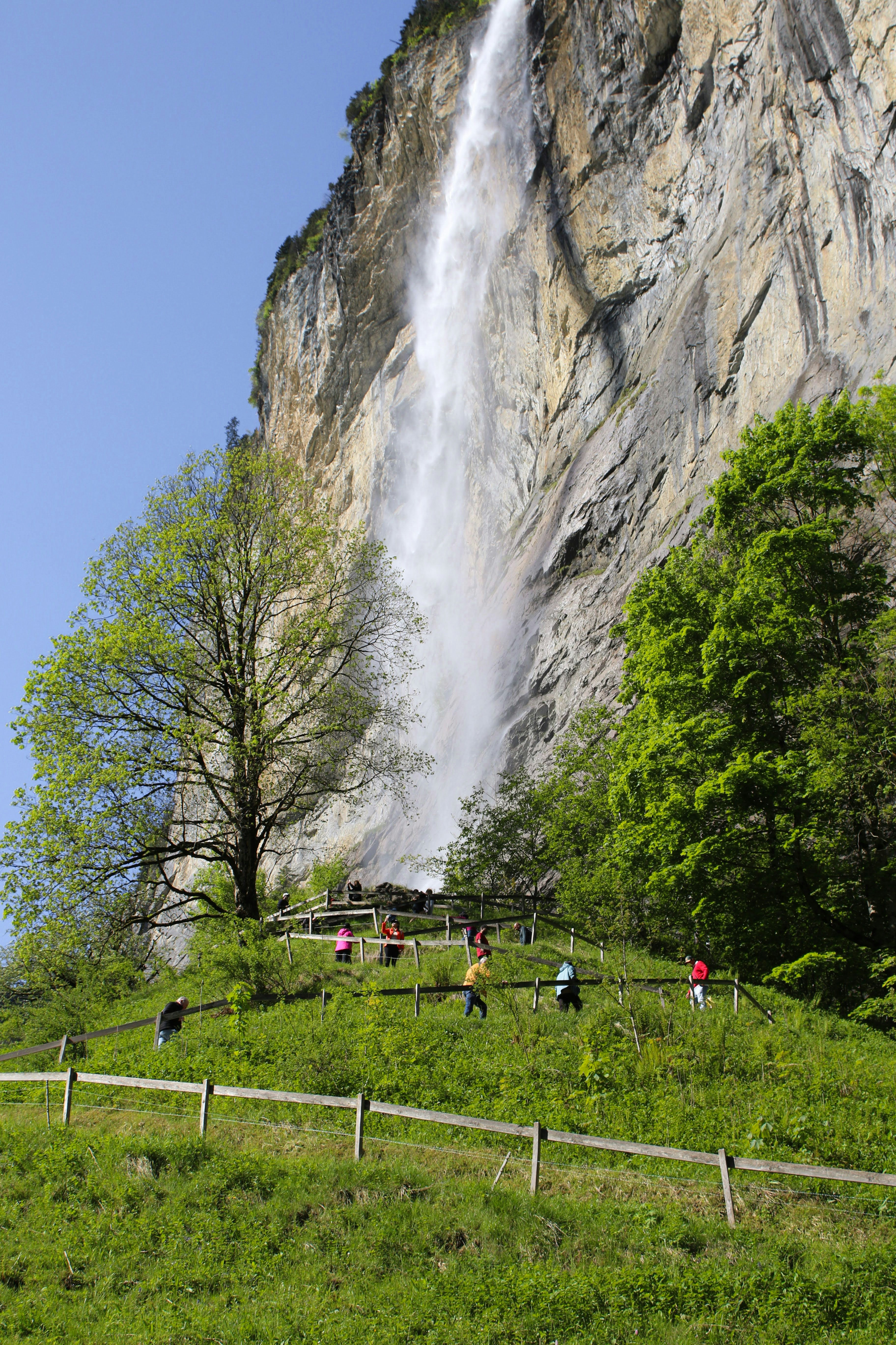 A majestic waterfall cascading down a rocky cliff, surrounded by vibrant greenery and visitors exploring the lush landscape.