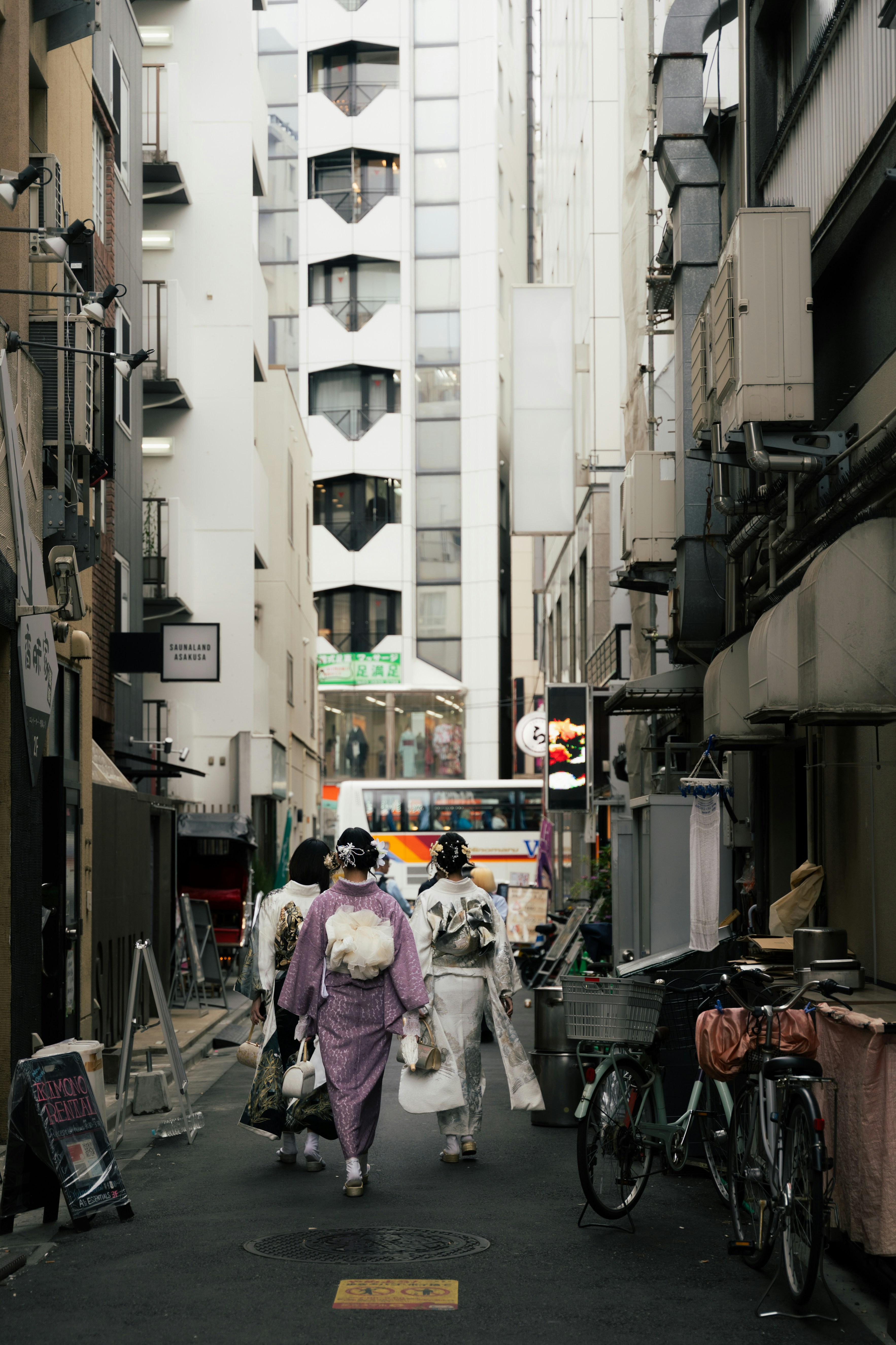 Women in kimonos walk down a narrow alleyway.