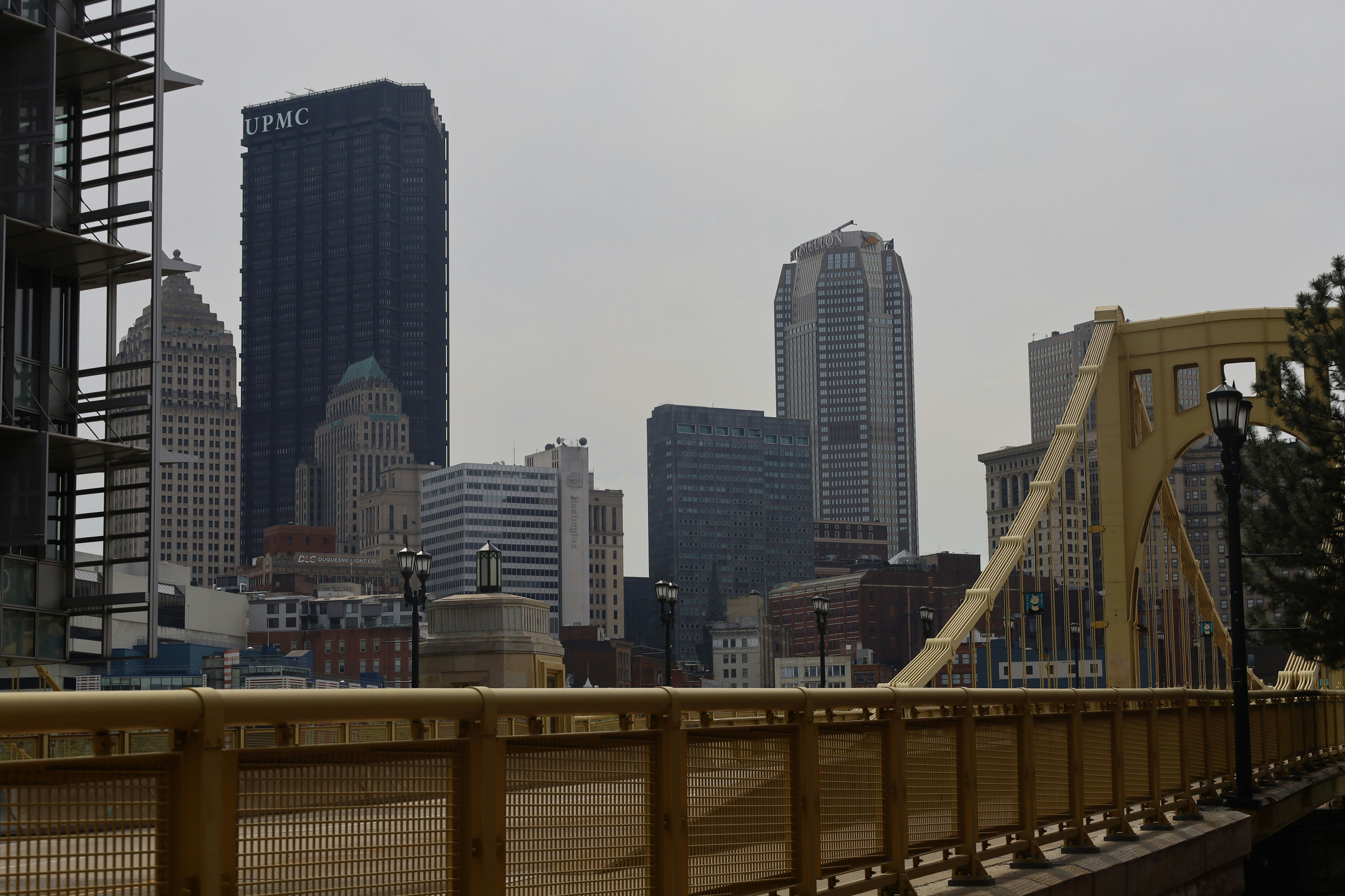 Golden bridge leading towards a skyline of modern skyscrapers under a hazy sky.