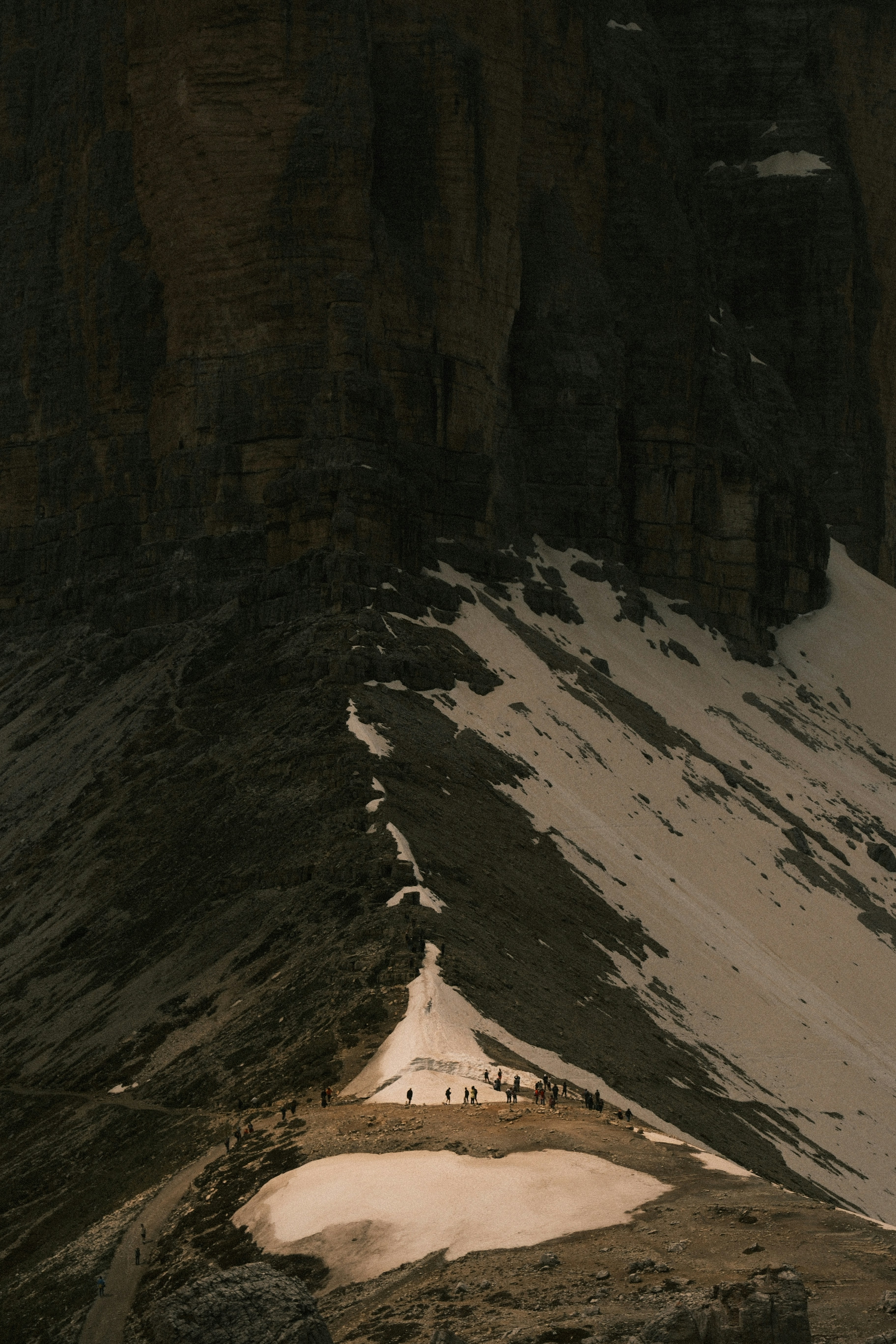 Hikers stand on snow beneath a massive mountain.