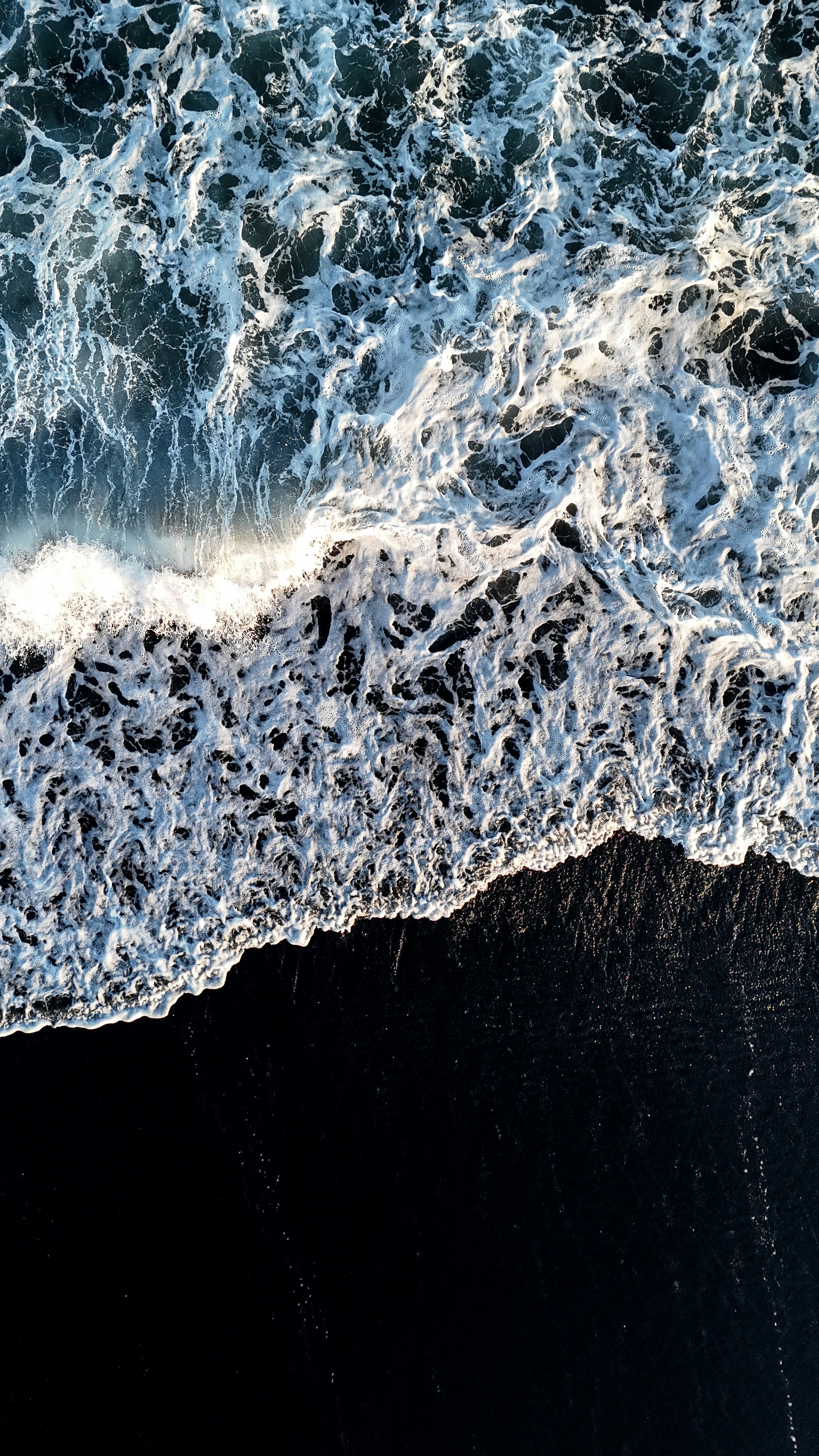 Foamy waves crash onto a dark, sandy beach.