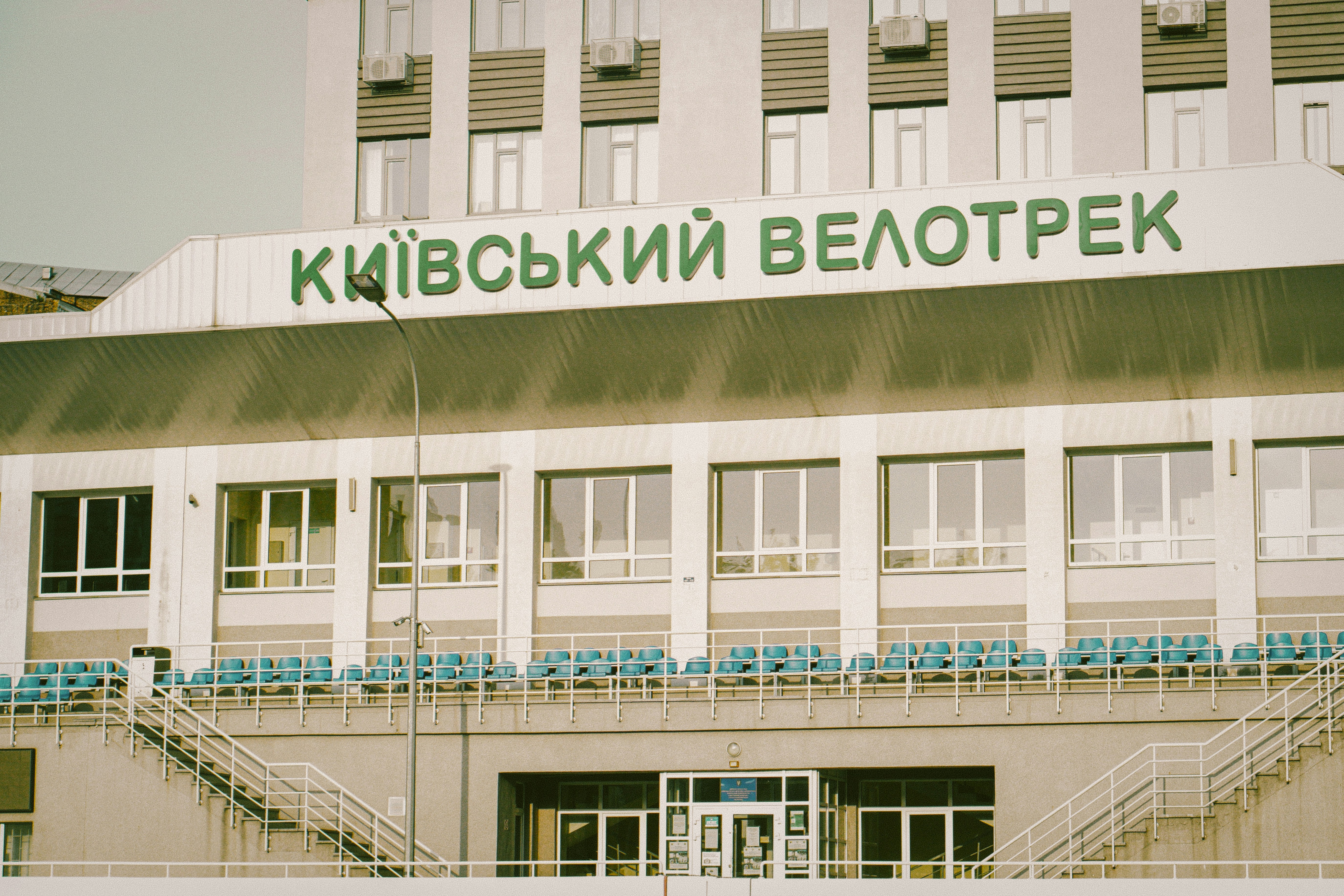Photographs taken at the Kyiv Velodrome, Ukraine, showcasing professional and amateur track cyclists during training sessions. The images highlight various aspects of velodrome cycling, including group riding, individual efforts, cycling gear, and the architectural features of the track. Captured in both color and monochrome for documentation and visual analysis. | The building says "kyiv velotrek" in ukrainian.
