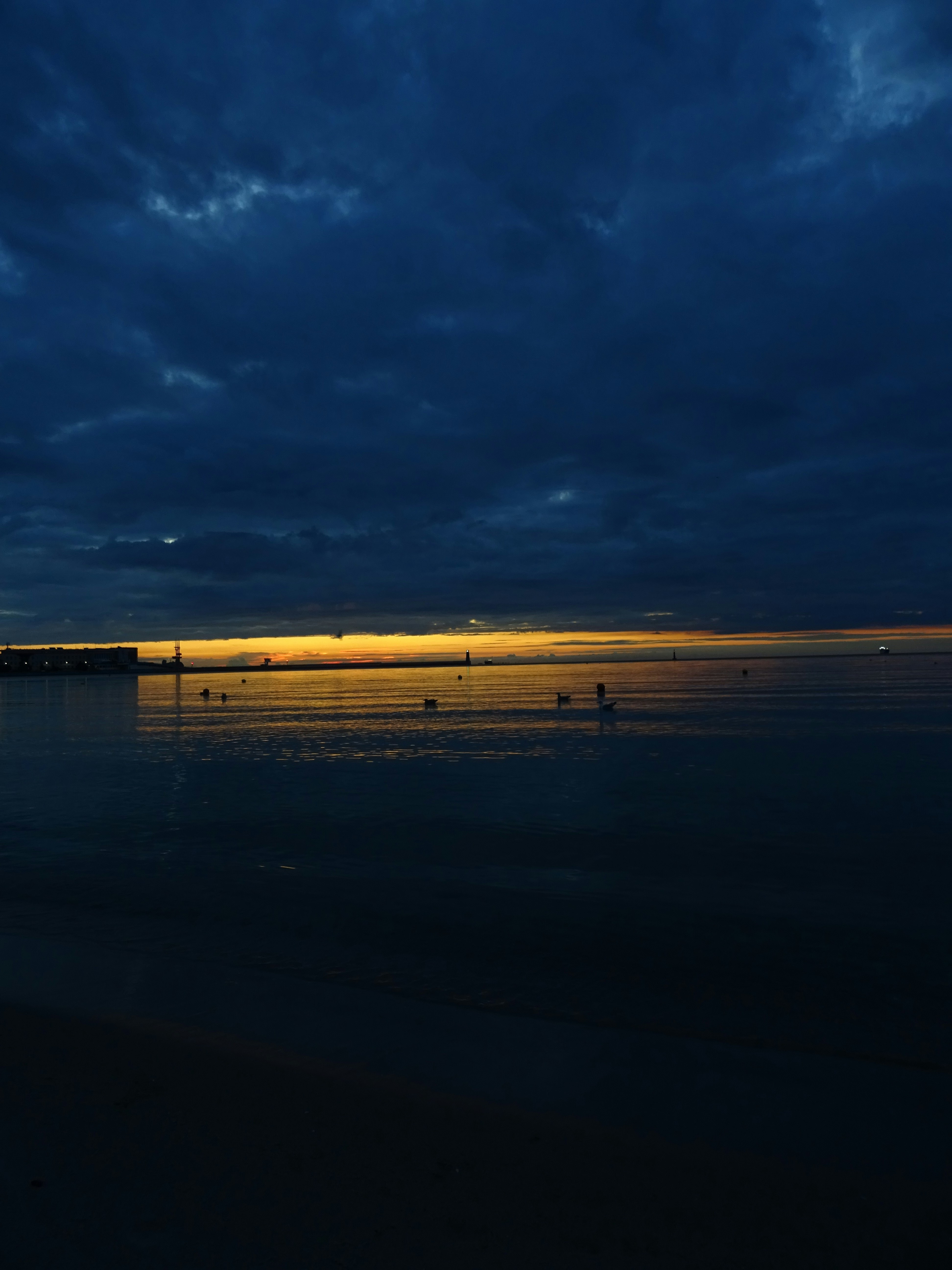 Evening sunset over calm water and a dark sky.