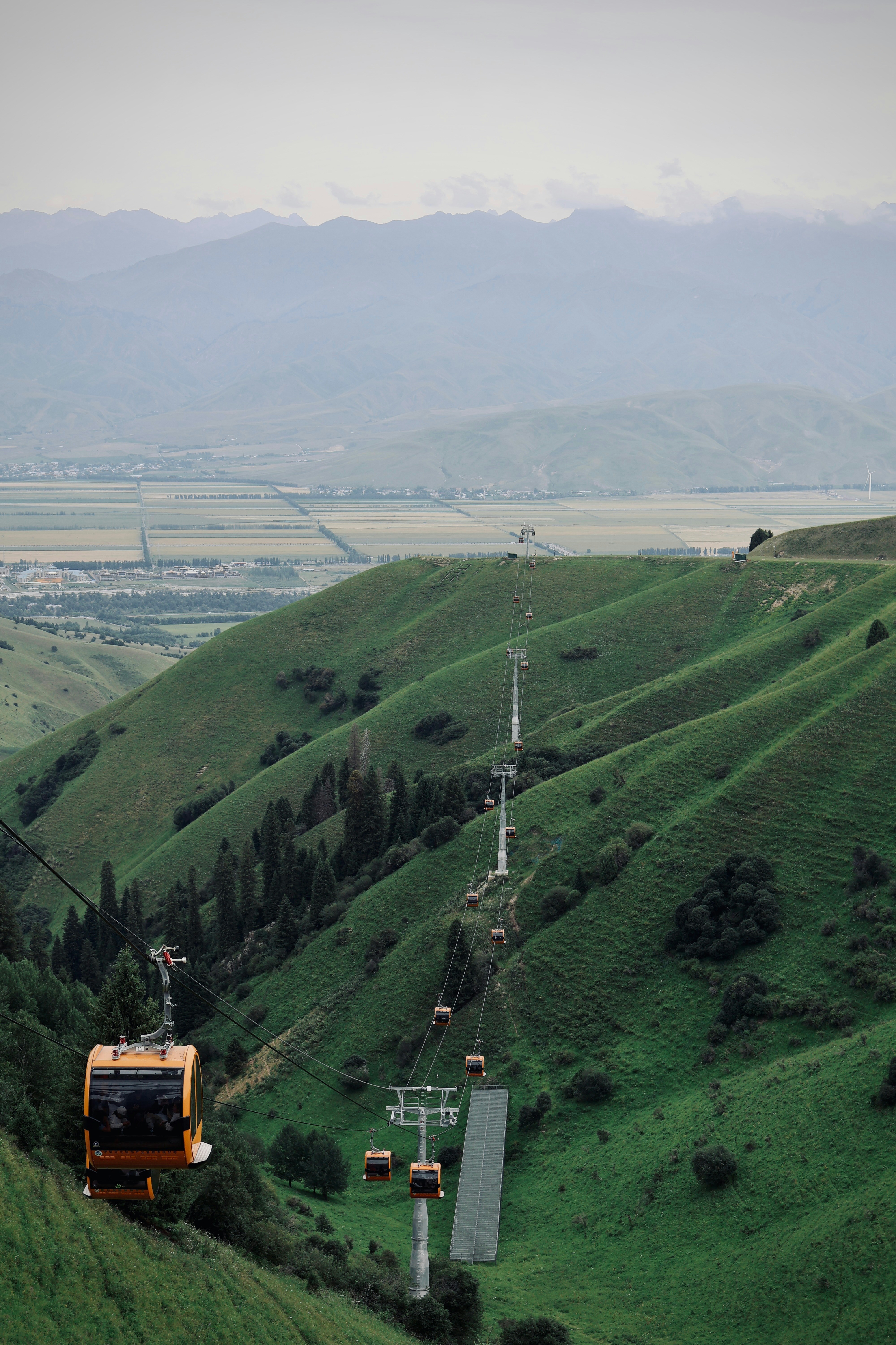 Cable car ascends a lush, green hillside landscape.
