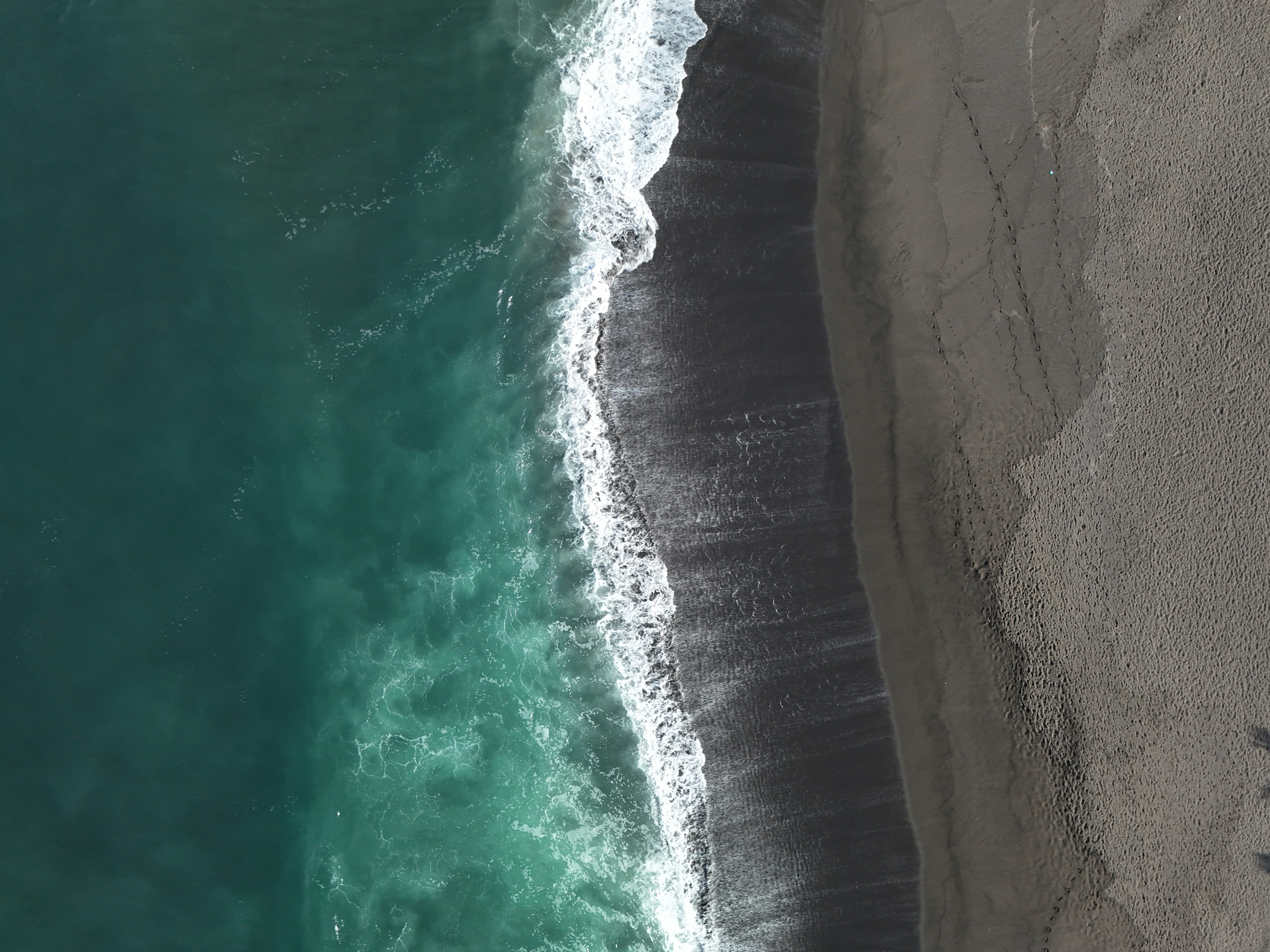 Bali Drone Shot | Waves crash onto a dark, sandy beach.