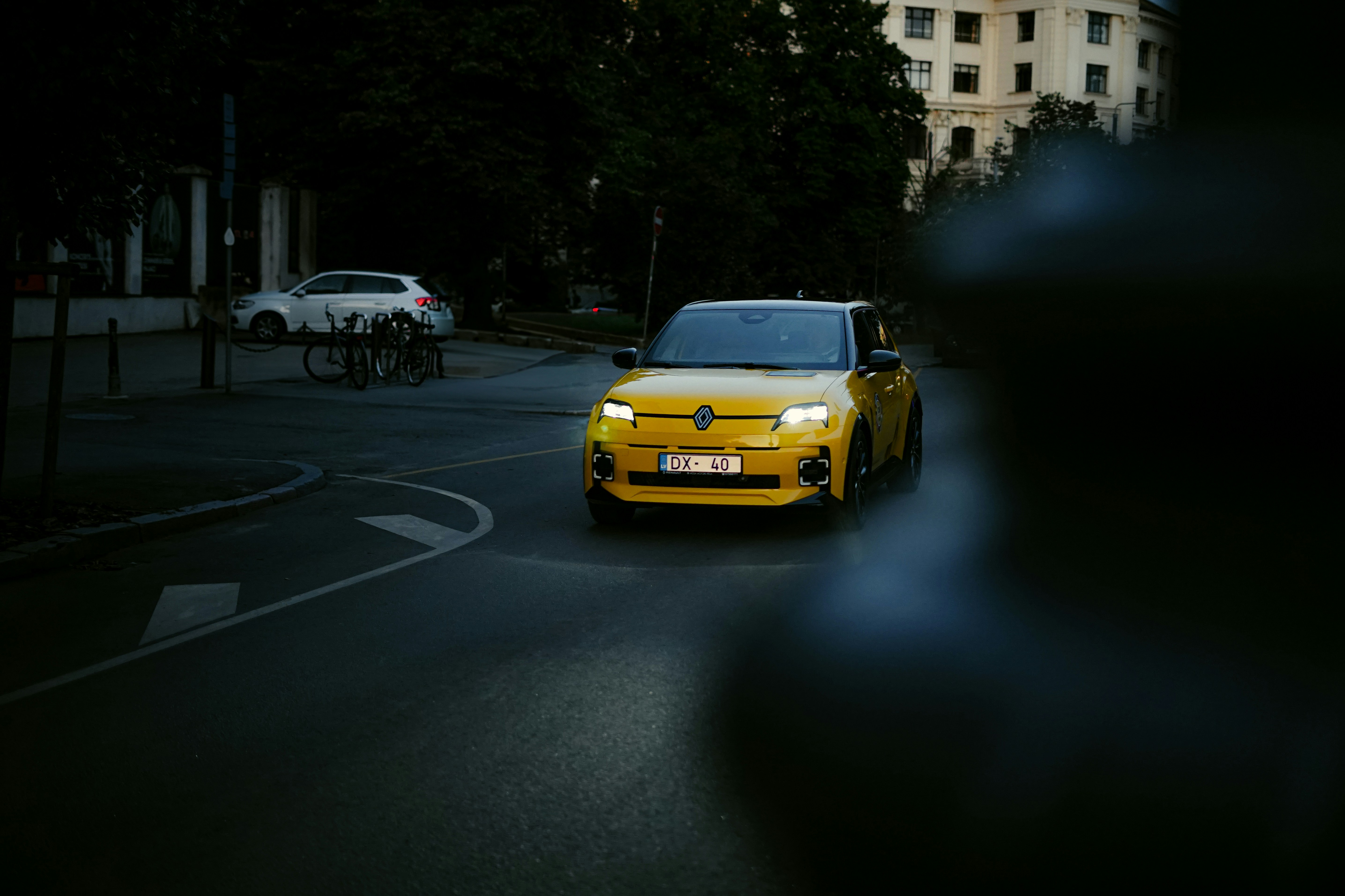 A vibrant yellow Renault car navigates a dimly lit urban street, surrounded by shadows and soft city lights.
