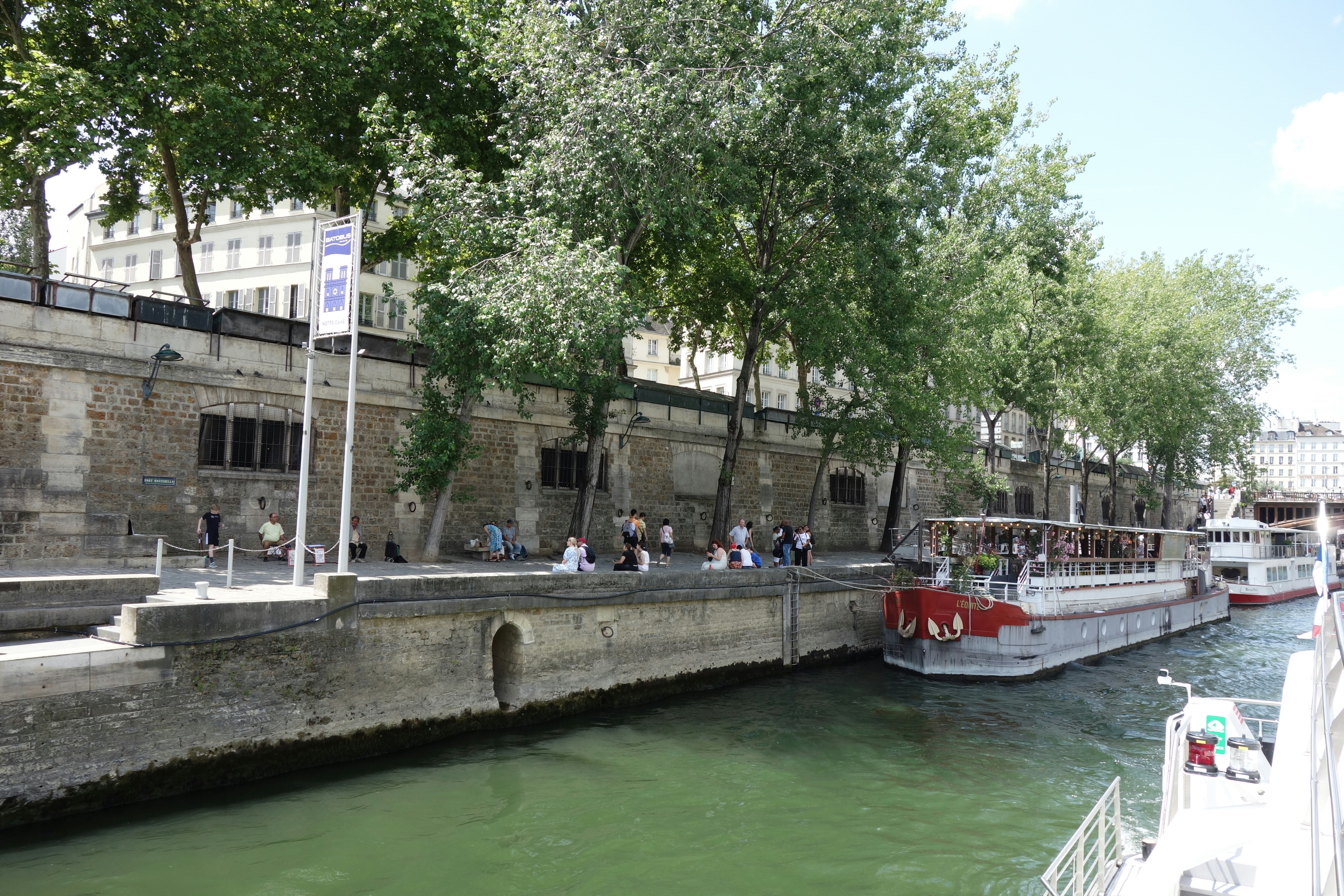 Boats sail on a river near a stone wall.