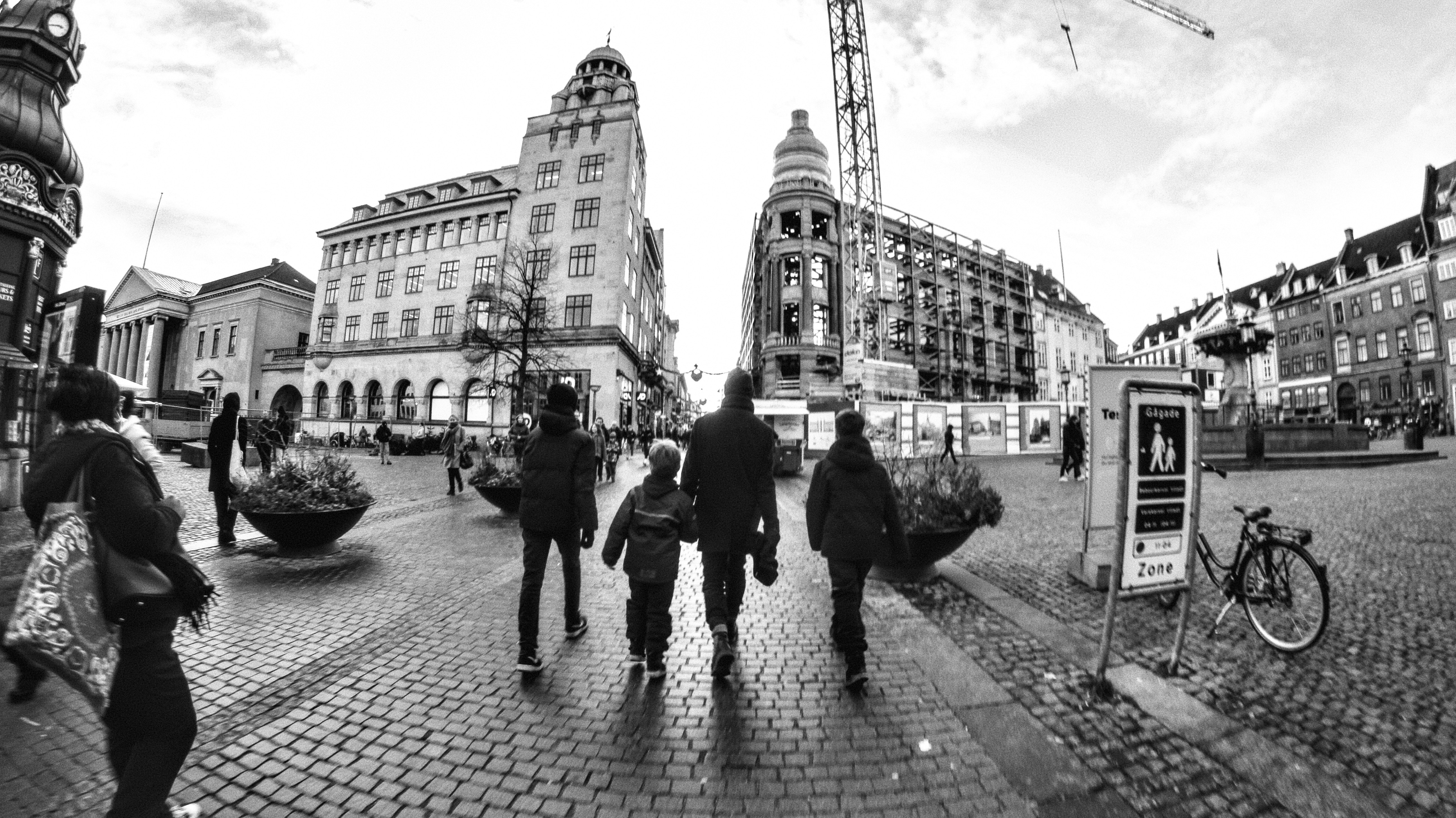 Walking on a street in Copenhagen alongside commuters. | People walk along a city street with buildings.