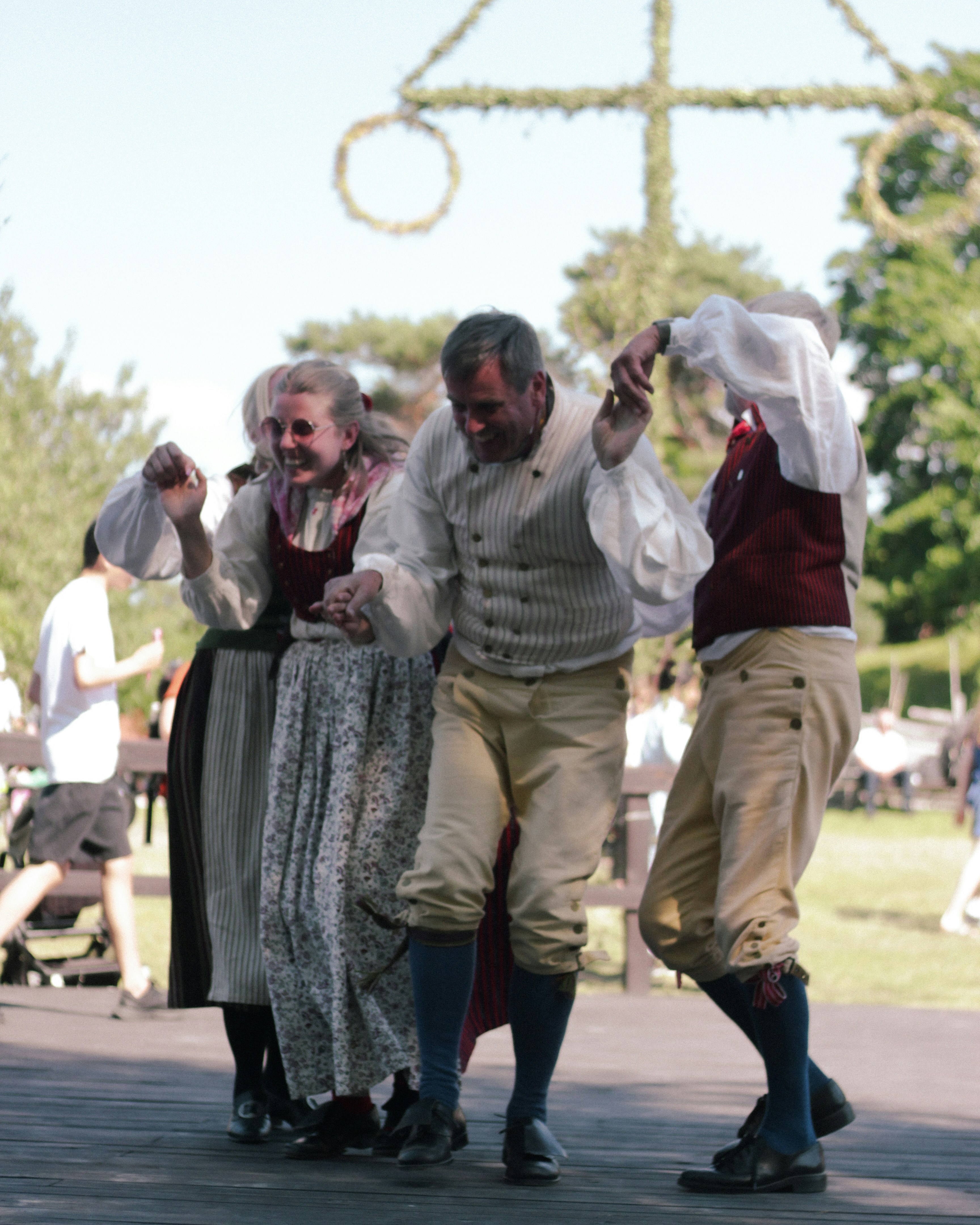 Watching Swedes dance during a Midsummer morning celebration. | People in traditional clothing dance together.