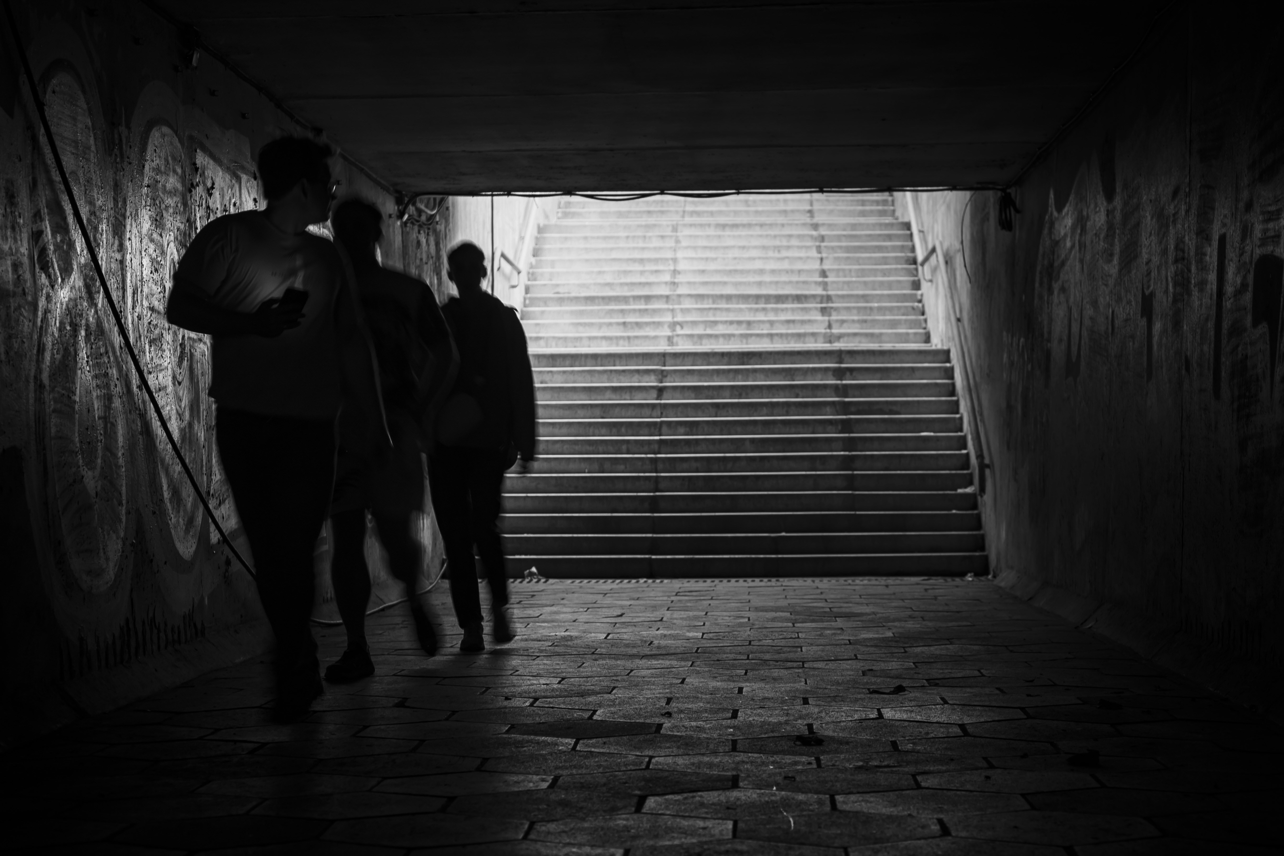 A group of people is walking through a dark underpass | Silhouetted figures walk towards stairs in a tunnel.