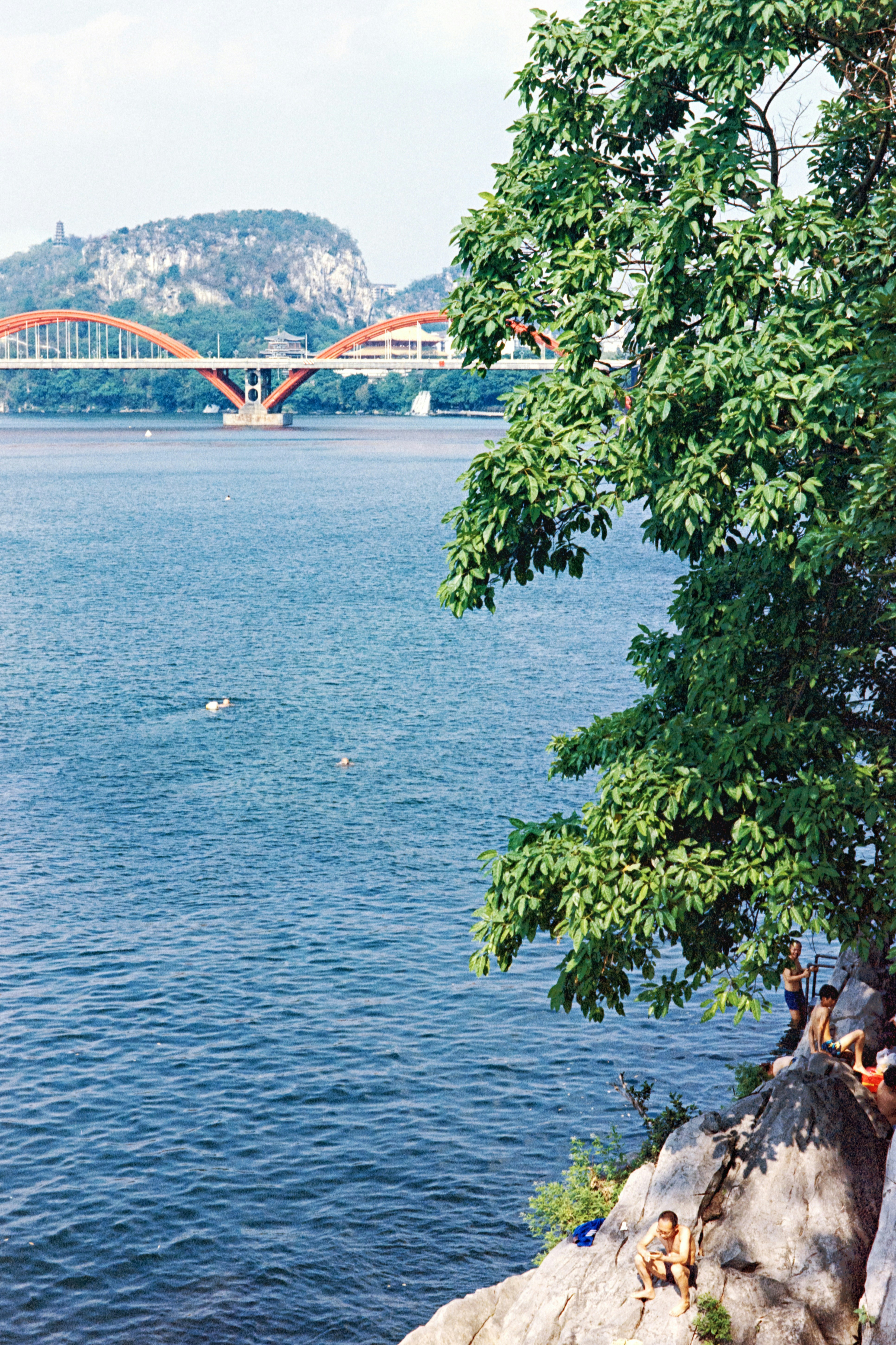 Orange Arch Over a Sapphire Lake: Cliffside Moment by the Bridge