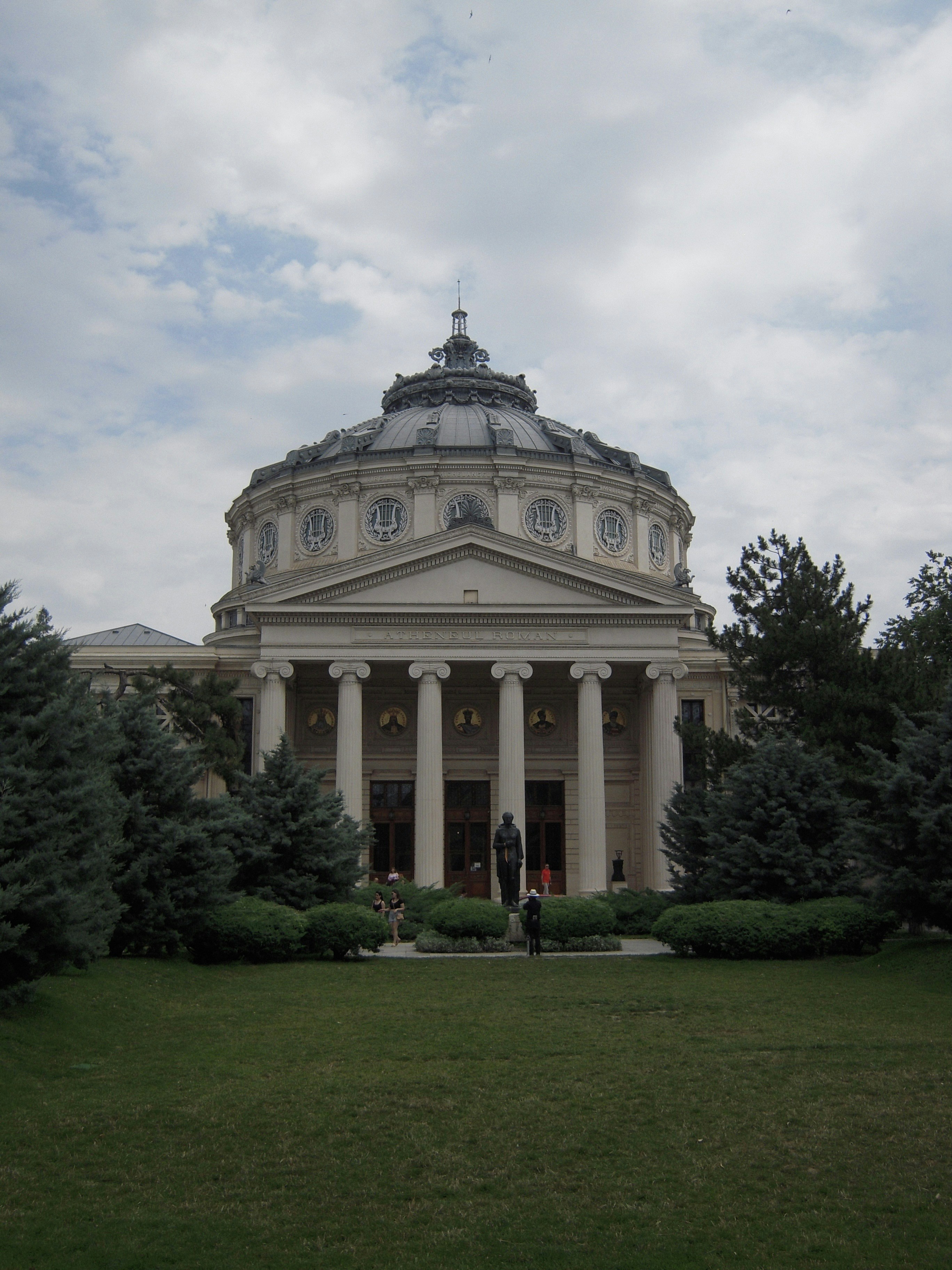 Ornate building with a prominent dome and classical columns, surrounded by lush greenery and visitors. A statue stands in front, adding to the historical ambiance.