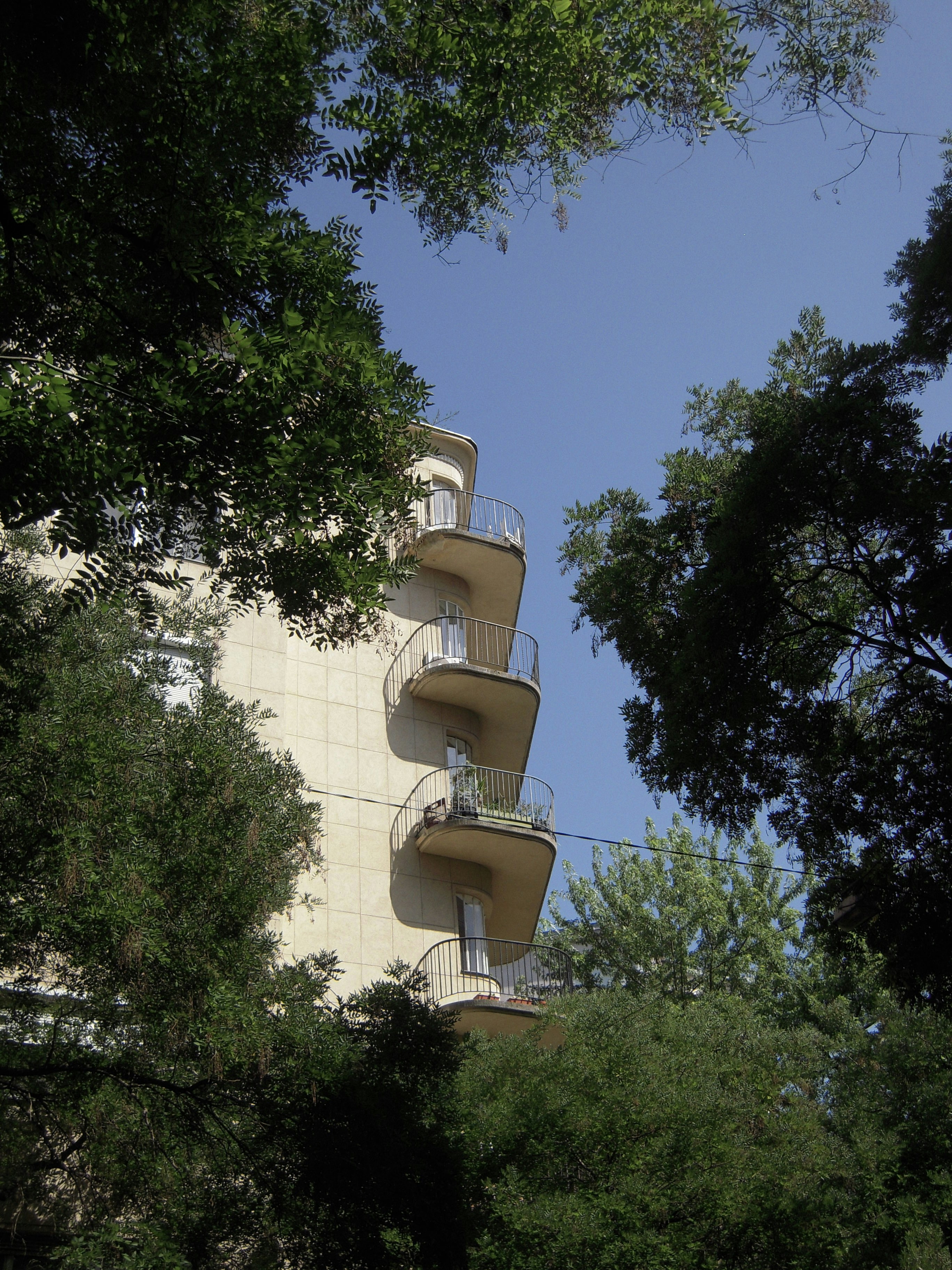Apartment balconies framed by green trees.