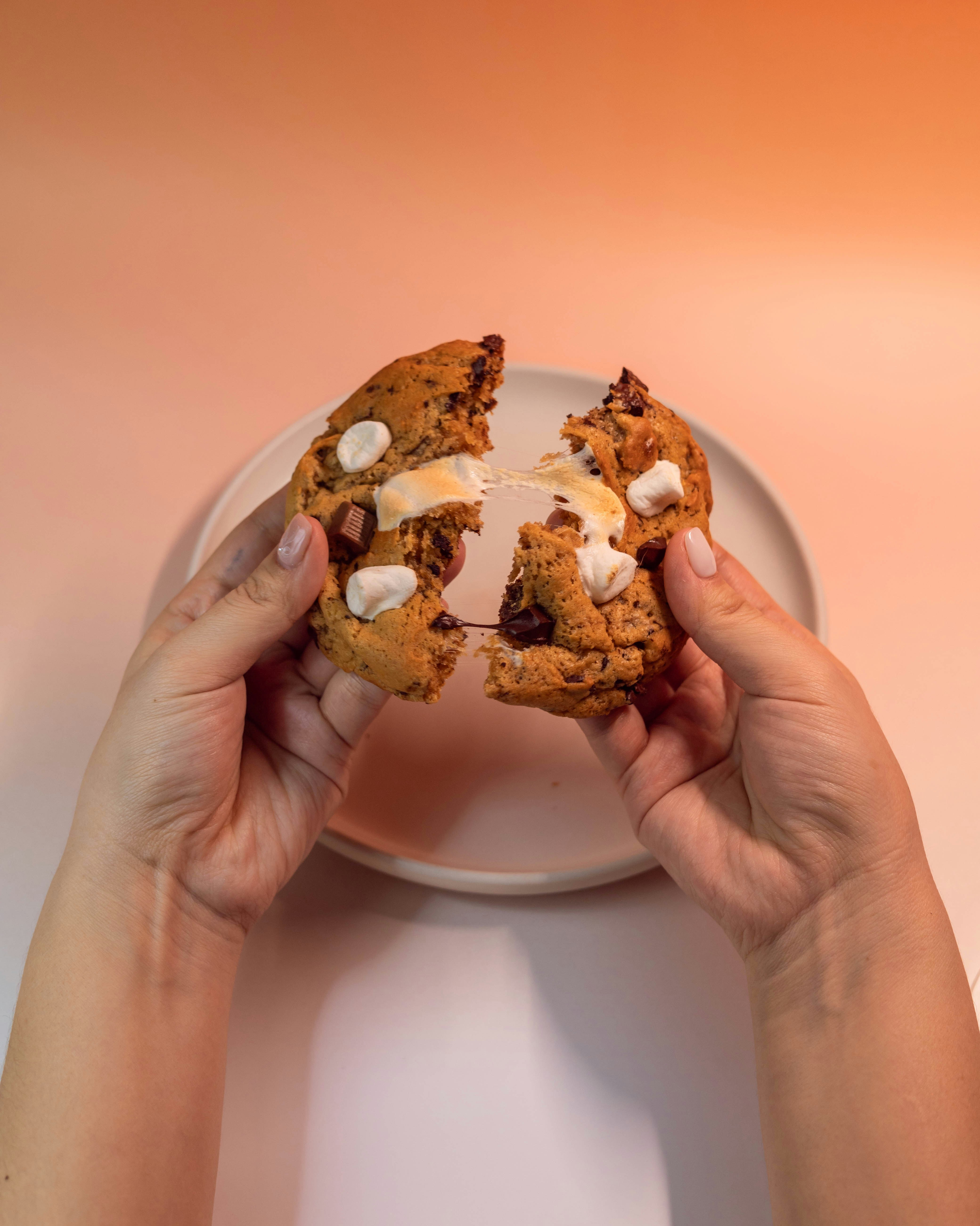 Cookie split: hands crumble a chocolate-chip treat over a pale plate